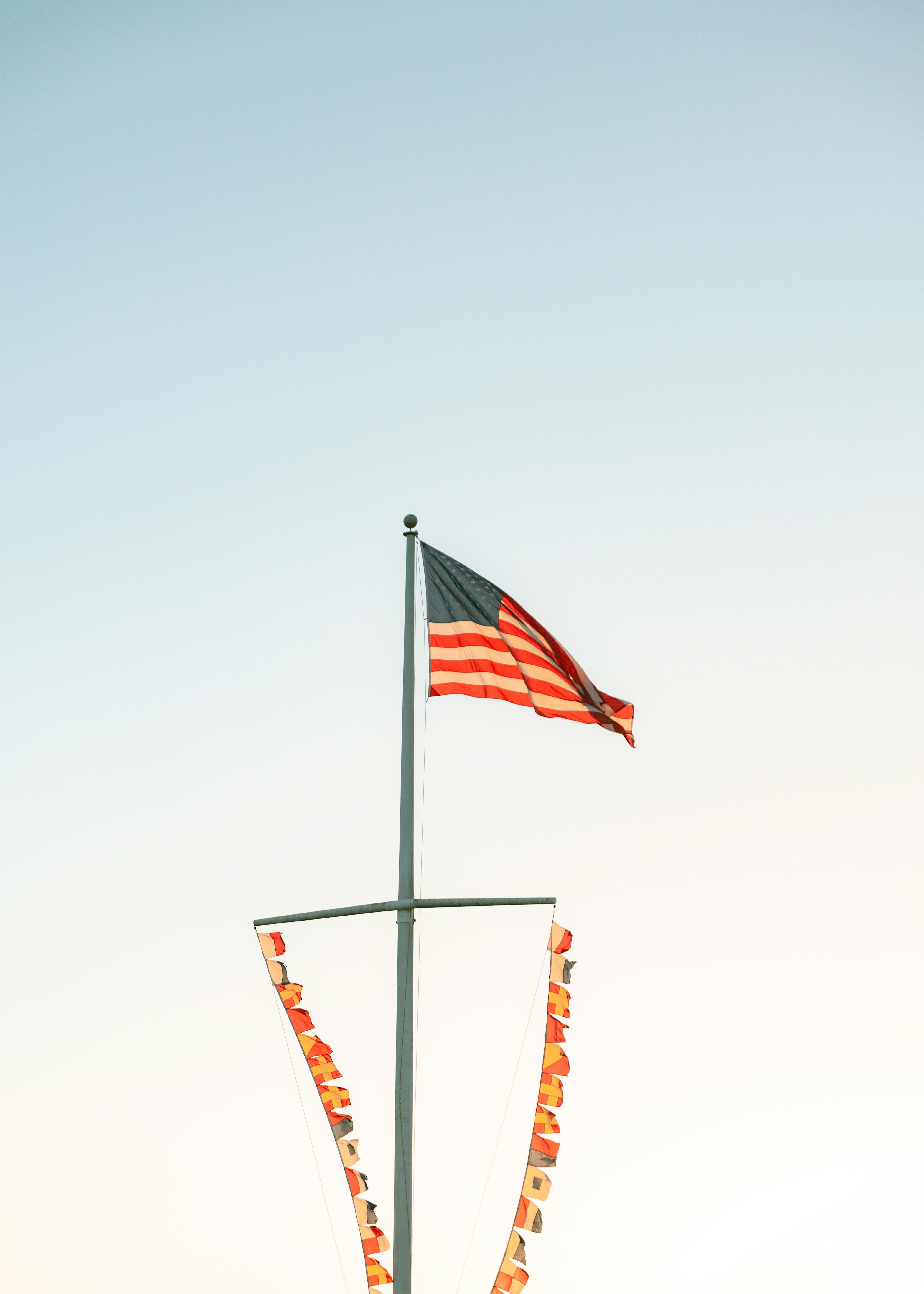 Pole of the Quiet Dawn: American Flag amid trailing pennants against a pale sky