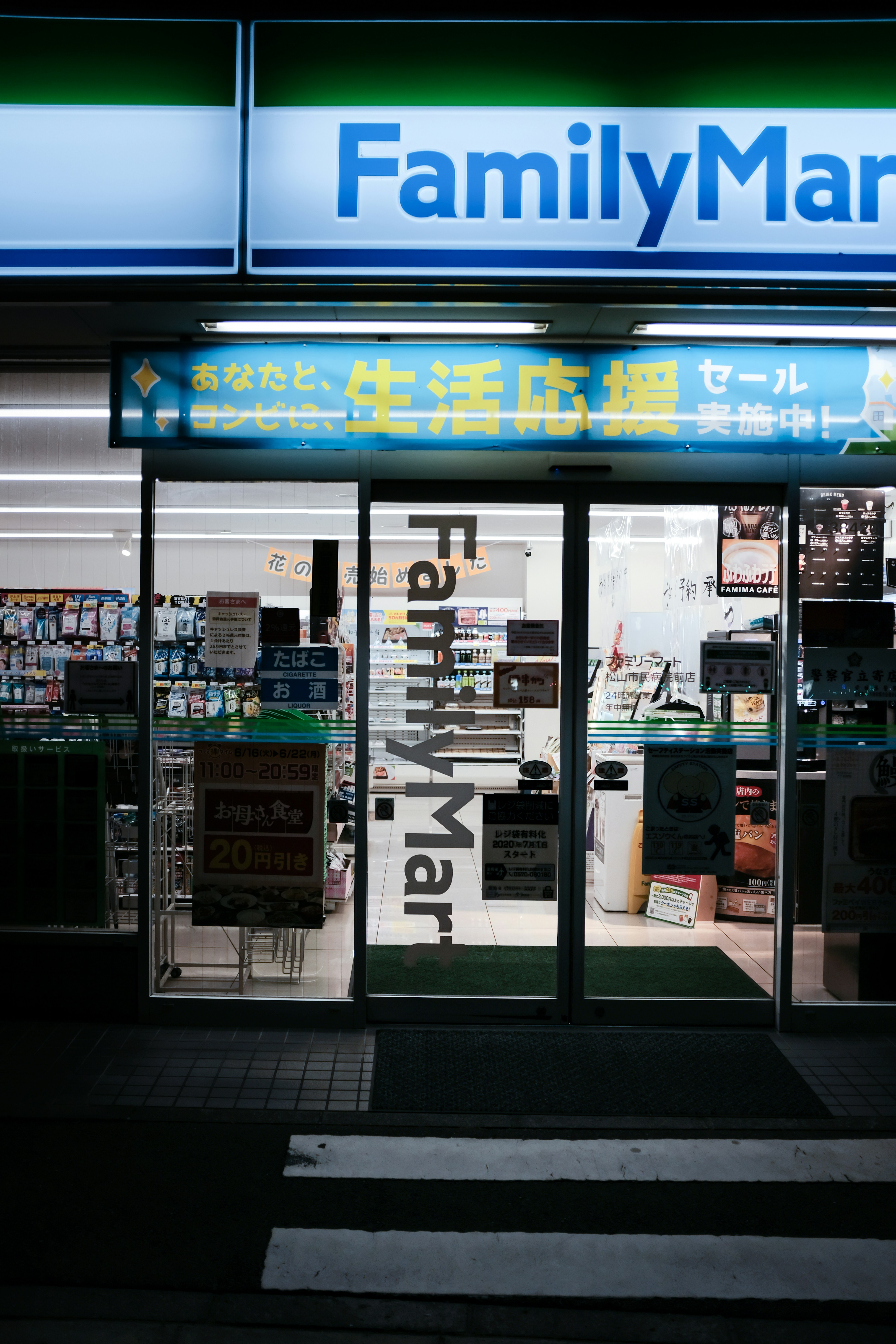 Brightly lit FamilyMart convenience store entrance at night, showcasing various products through glass doors.