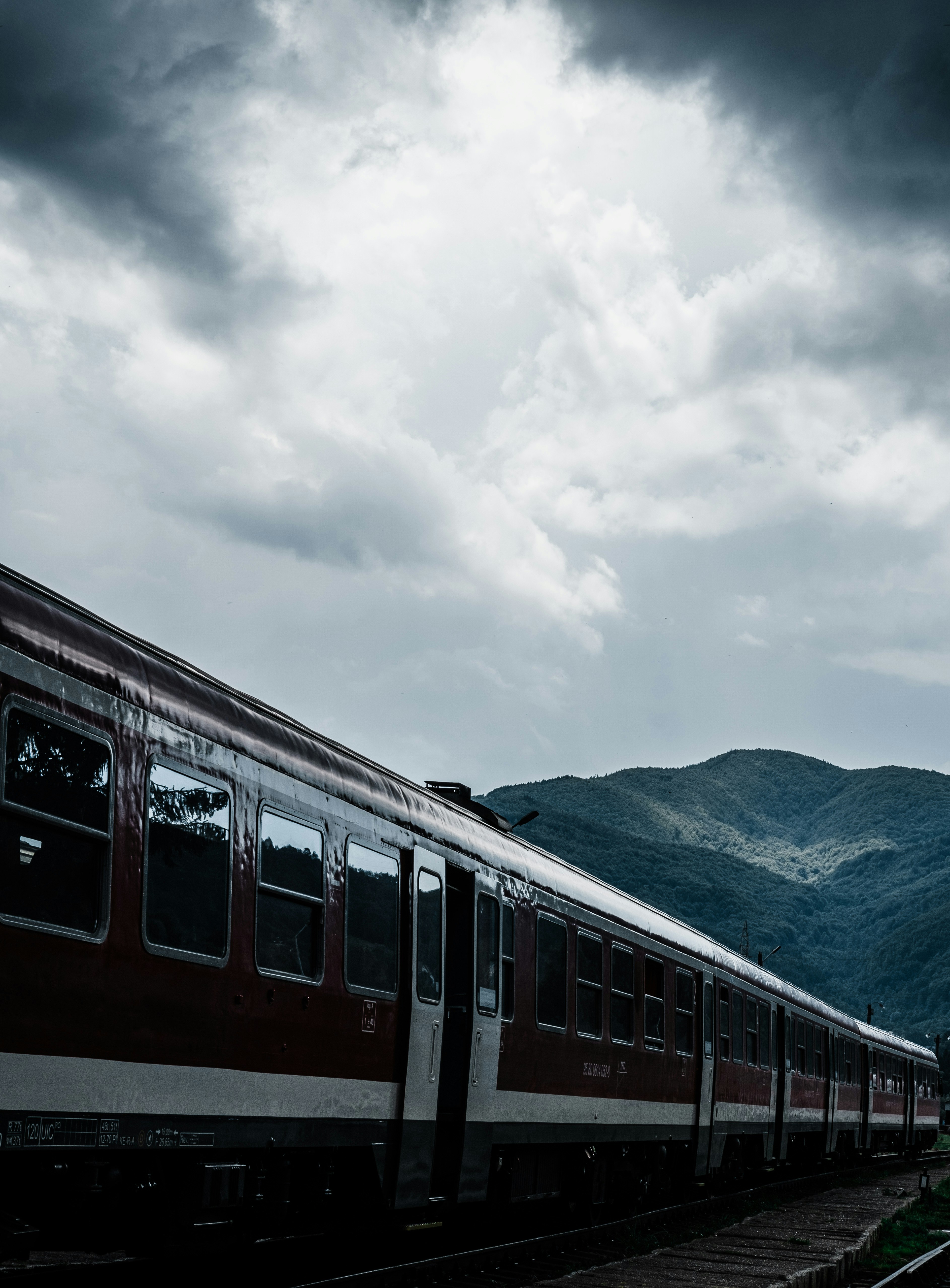 A vintage train sits quietly on the tracks, framed by rolling hills under a dramatic sky. The scene evokes a sense of nostalgia and adventure.