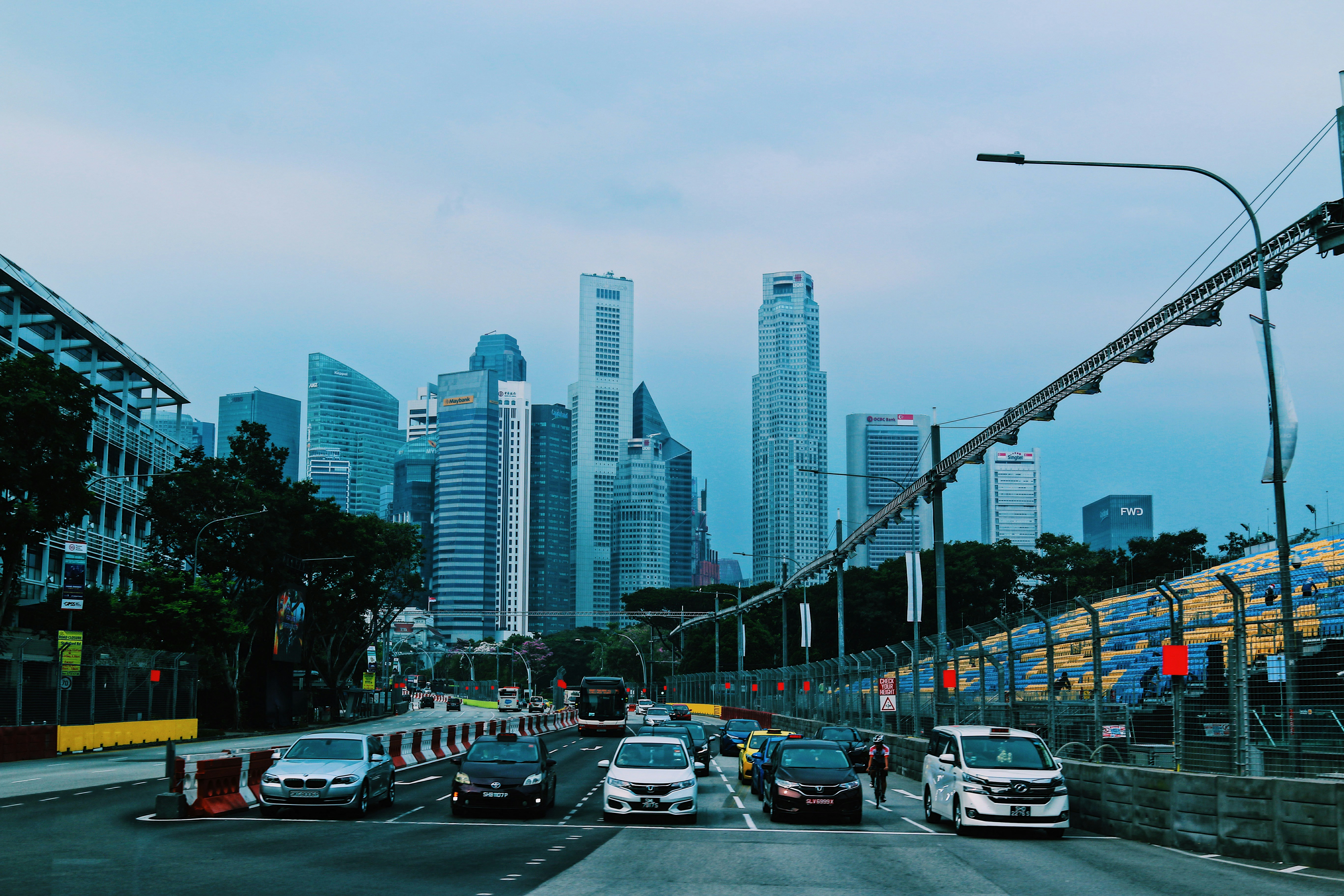 City skyline featuring modern skyscrapers along a busy street, with cars navigating the road under a moody sky.