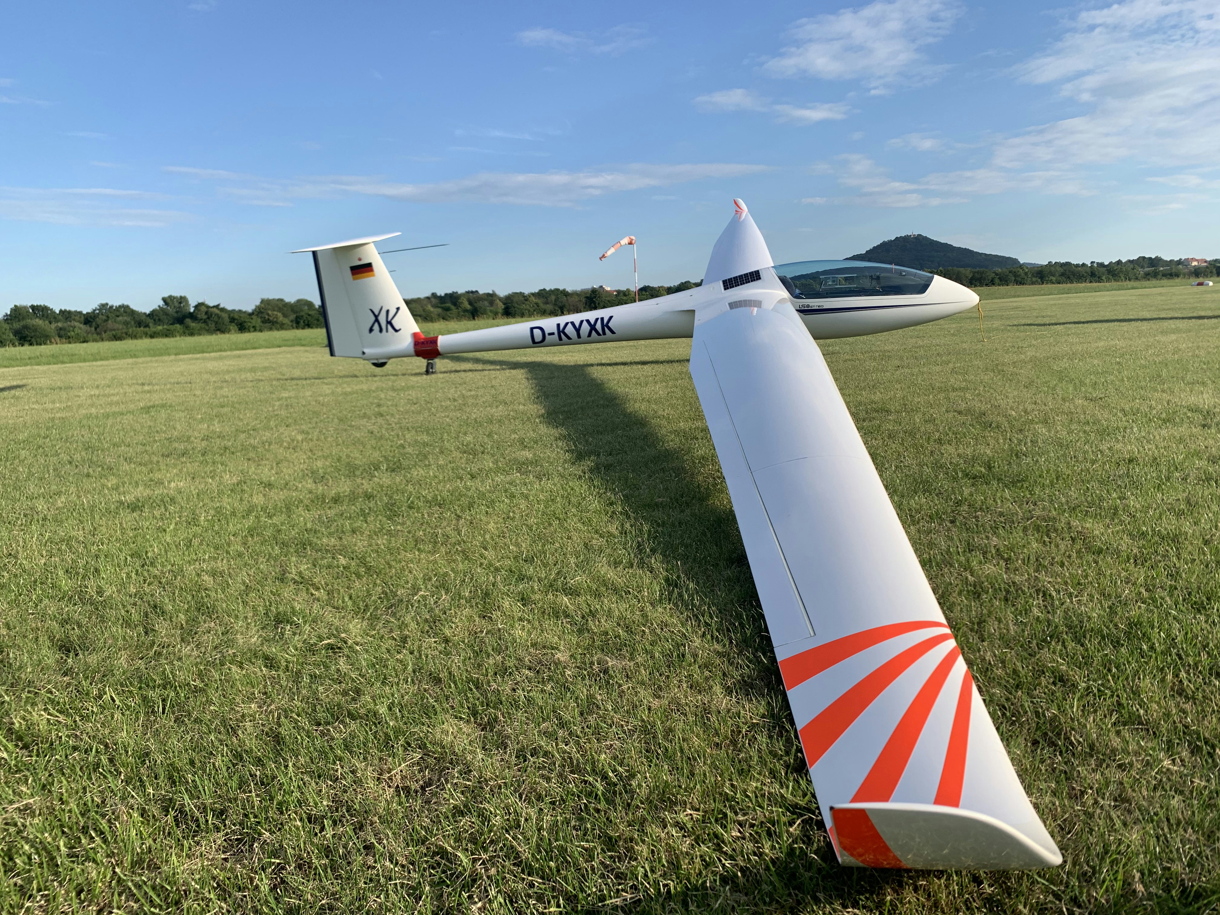 White glider with red accents parked on a grassy field under a clear blue sky.