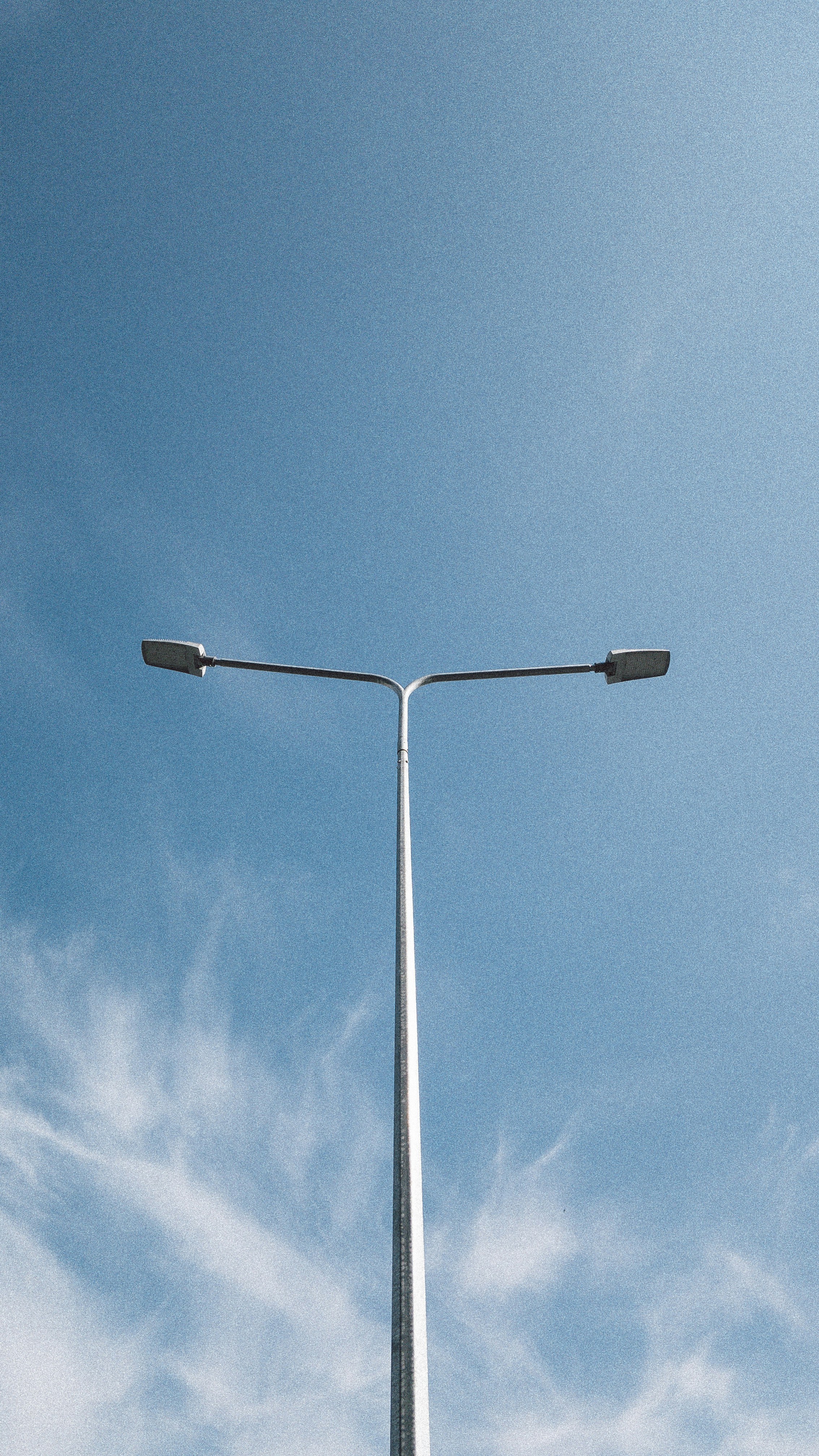 A sleek streetlight reaching towards a clear blue sky, framed by wispy clouds.