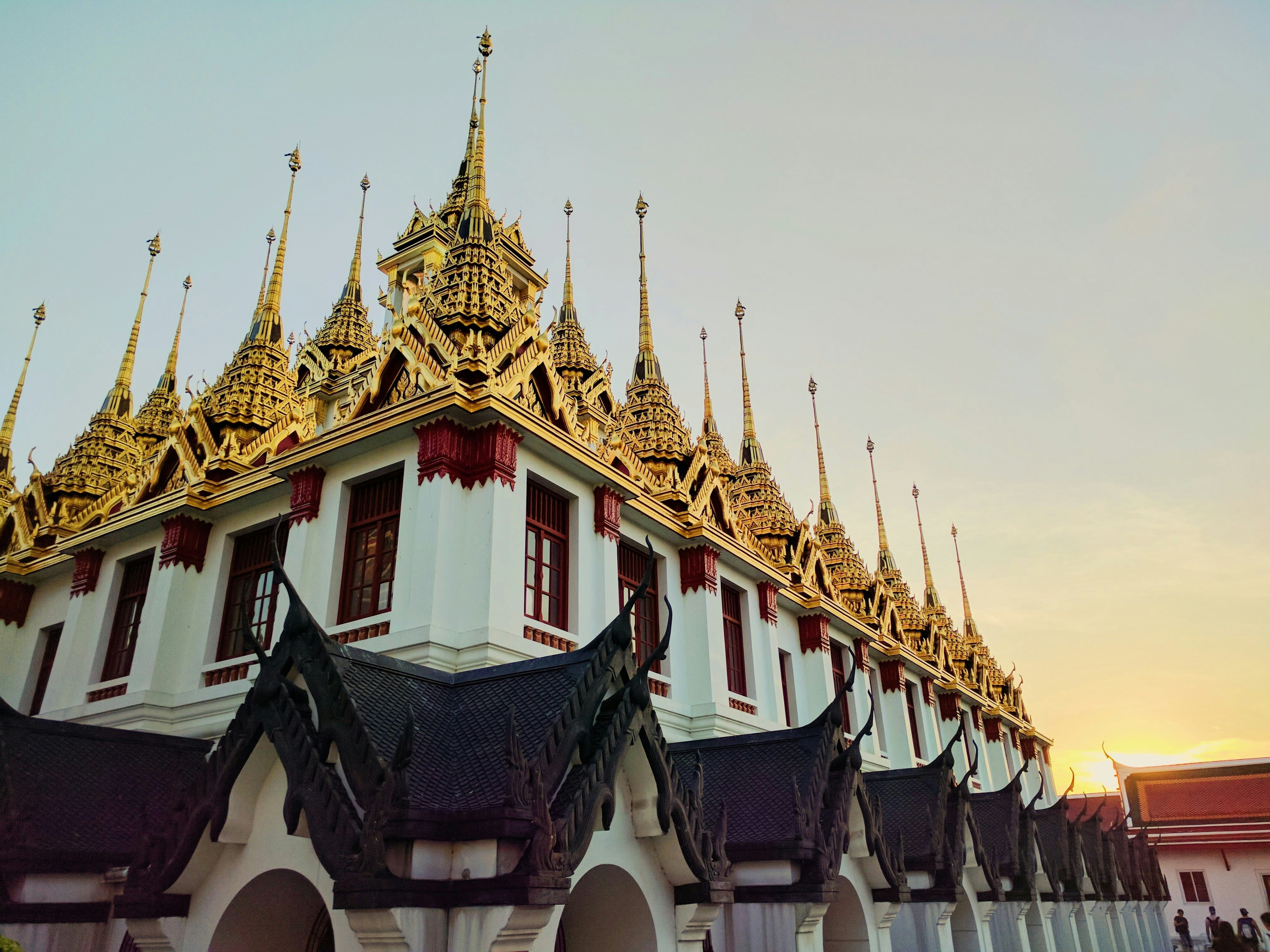 Ornate temple roof with a forest of gold spires rises above dark, tiered eaves against a warm dusk sky.