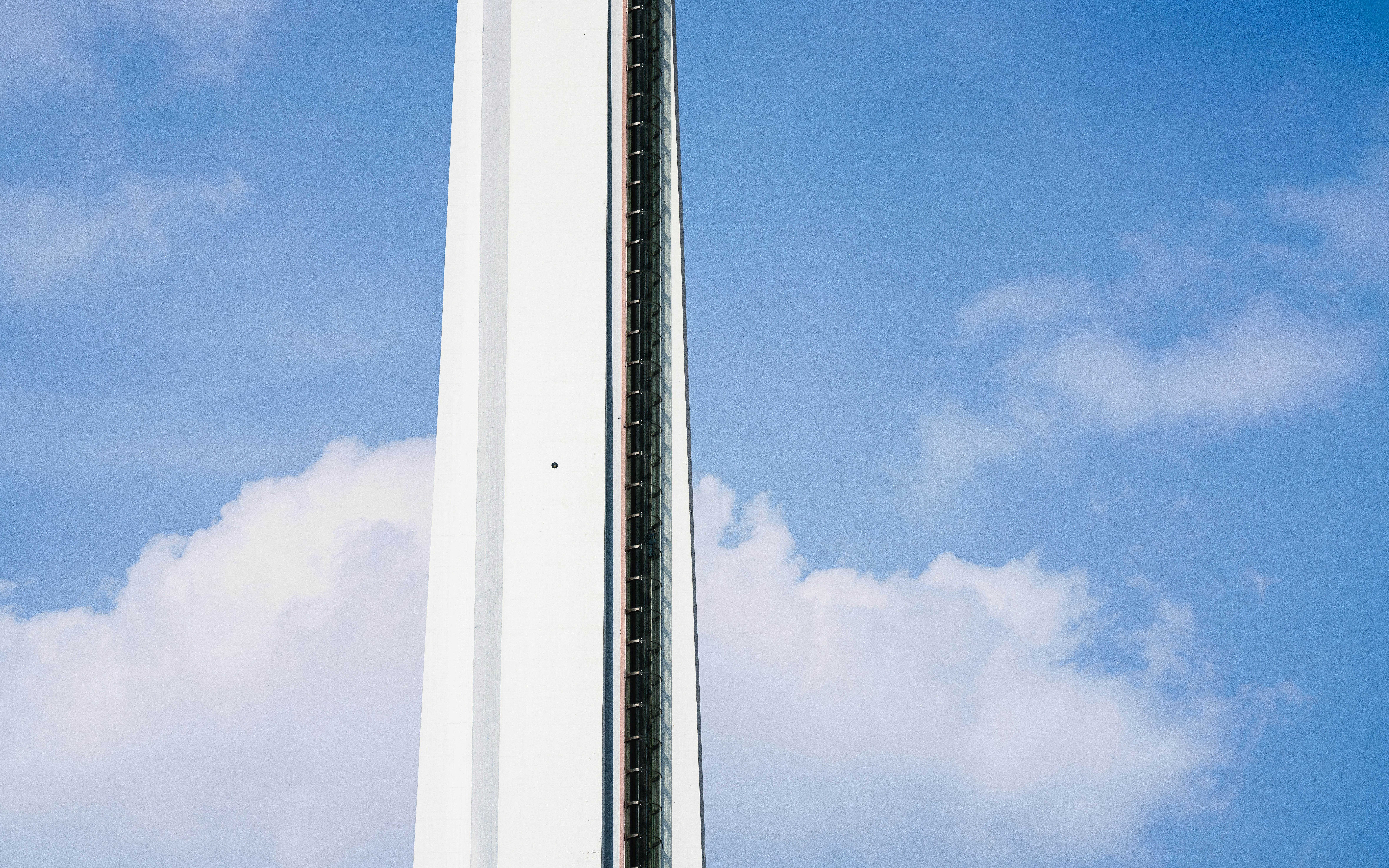 A sleek architectural tower rises against a backdrop of fluffy clouds and blue sky, showcasing a modern design. The image emphasizes the tower's height and structure.