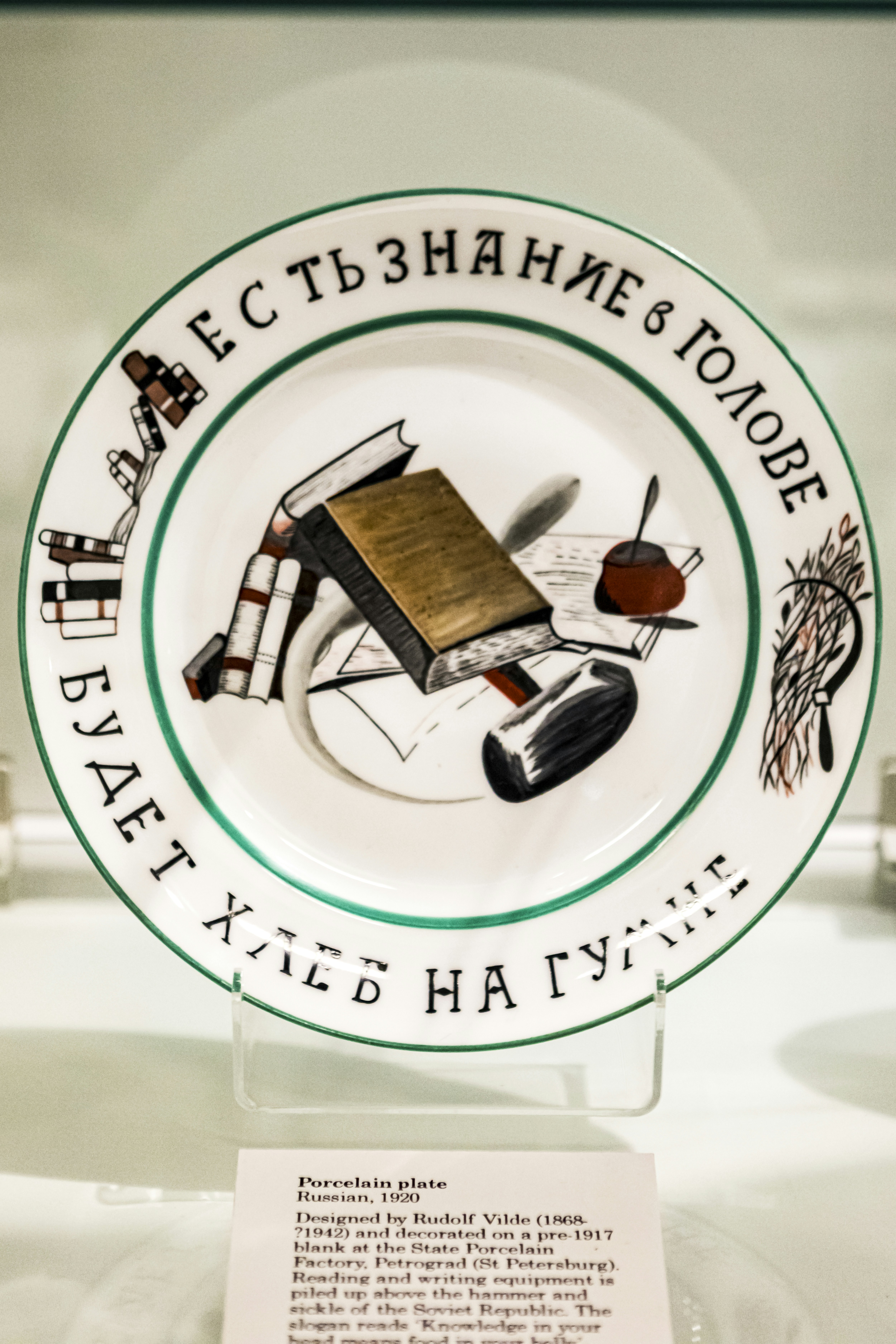 Decorative porcelain plate featuring an artistic depiction of books, a quill, and a cup, surrounded by a thoughtful inscription. A unique blend of art and literature.