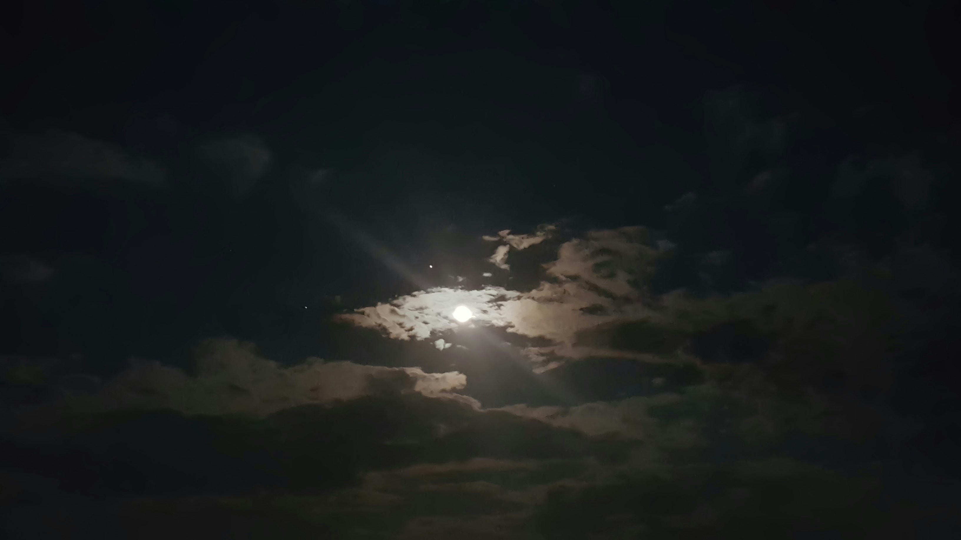 Moonlight breaking through scattered clouds in a dark night sky.