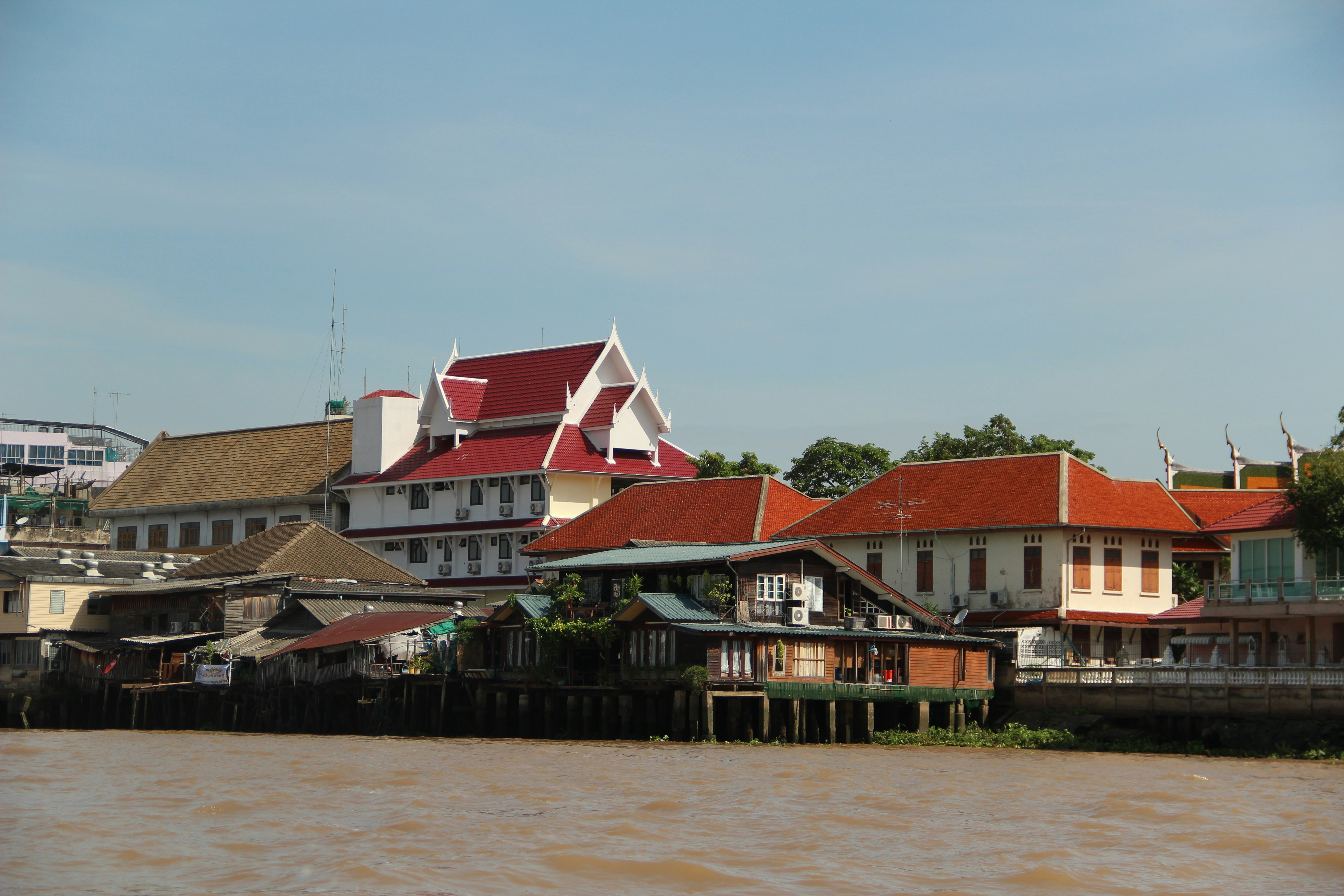 Traditional riverside buildings with distinct red roofs and intricate designs, reflecting cultural heritage along a flowing river.