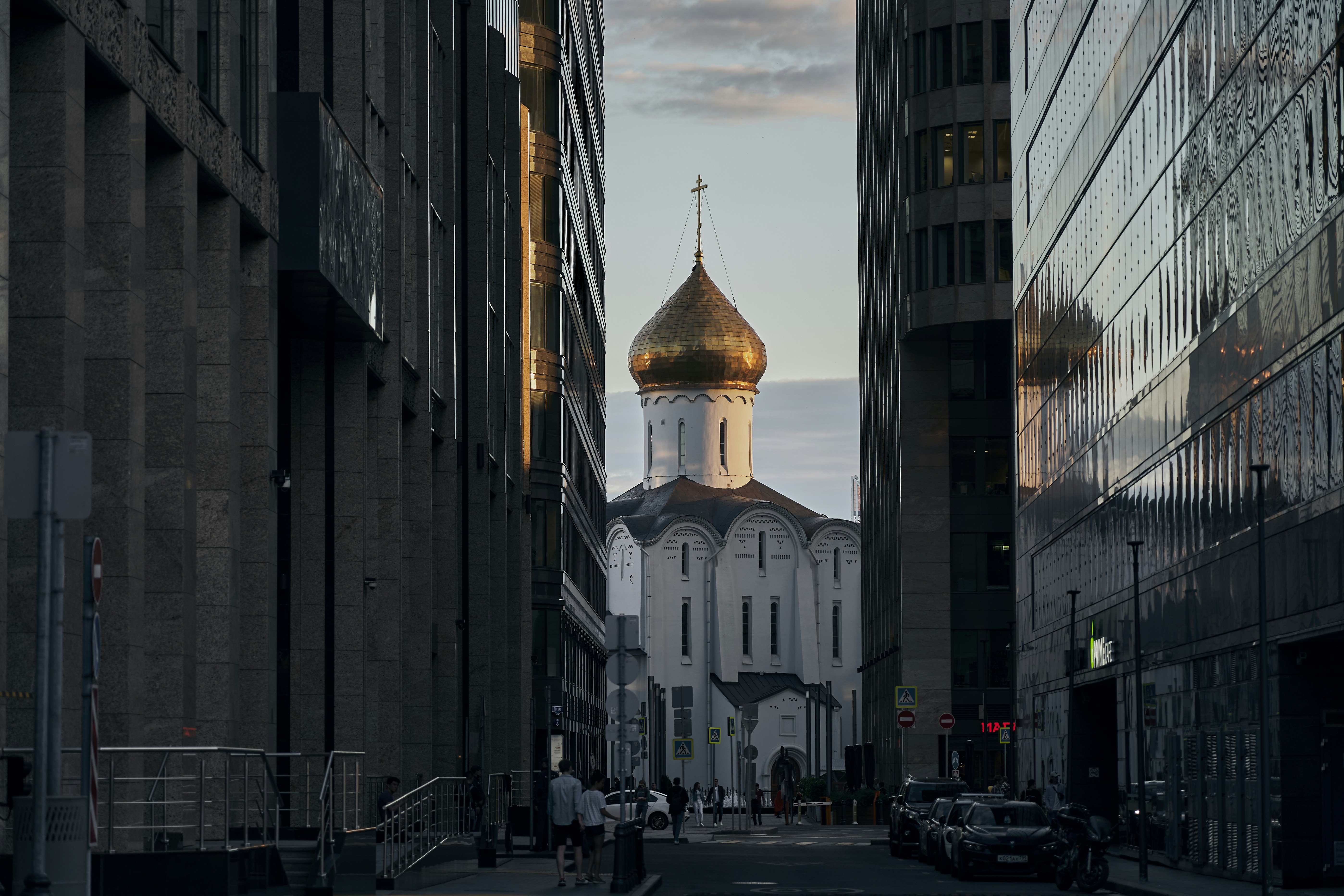 White church with golden dome framed by towering urban buildings at dusk.