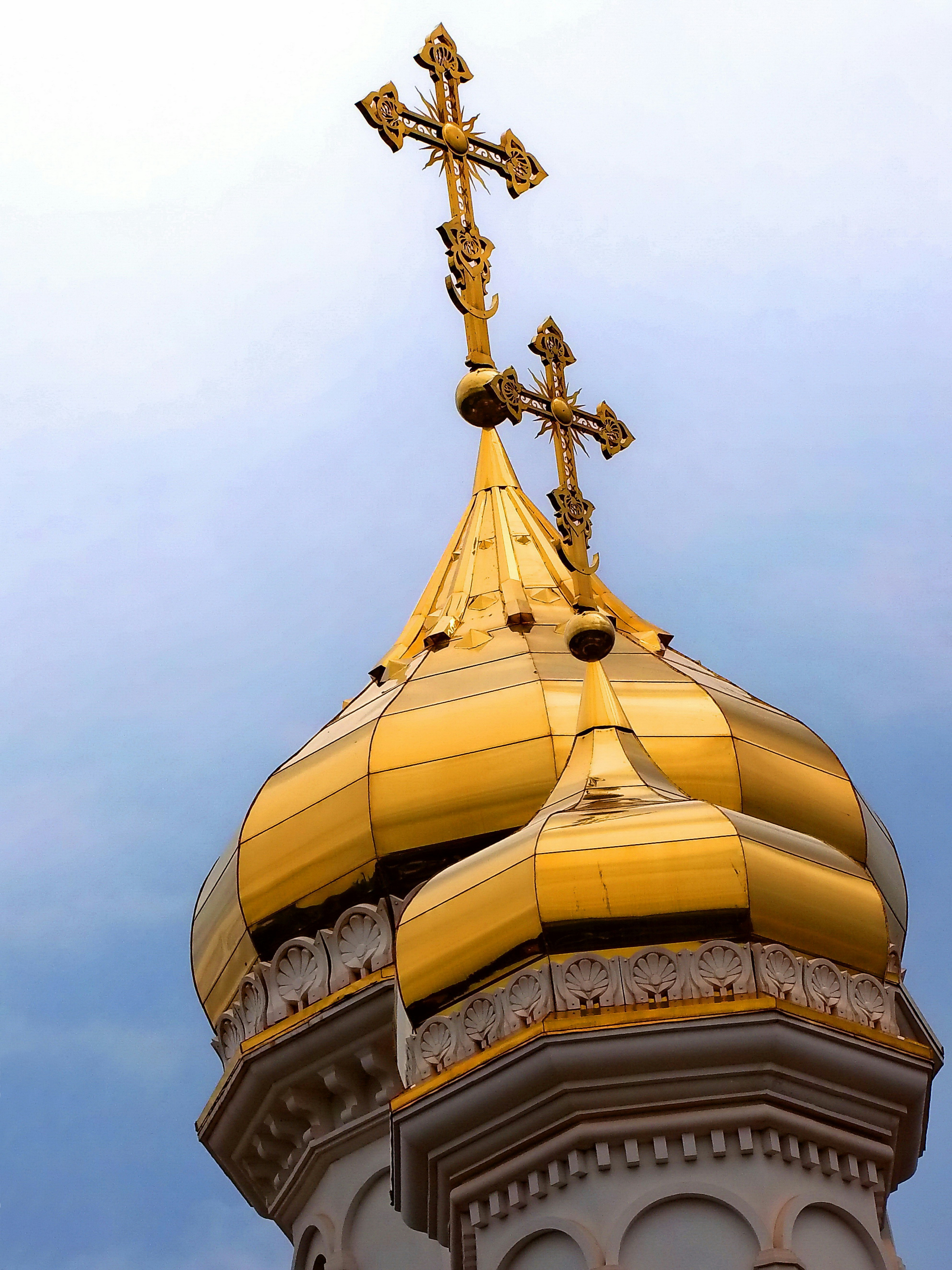 Golden dome of a church topped with ornate crosses against a cloudy sky.