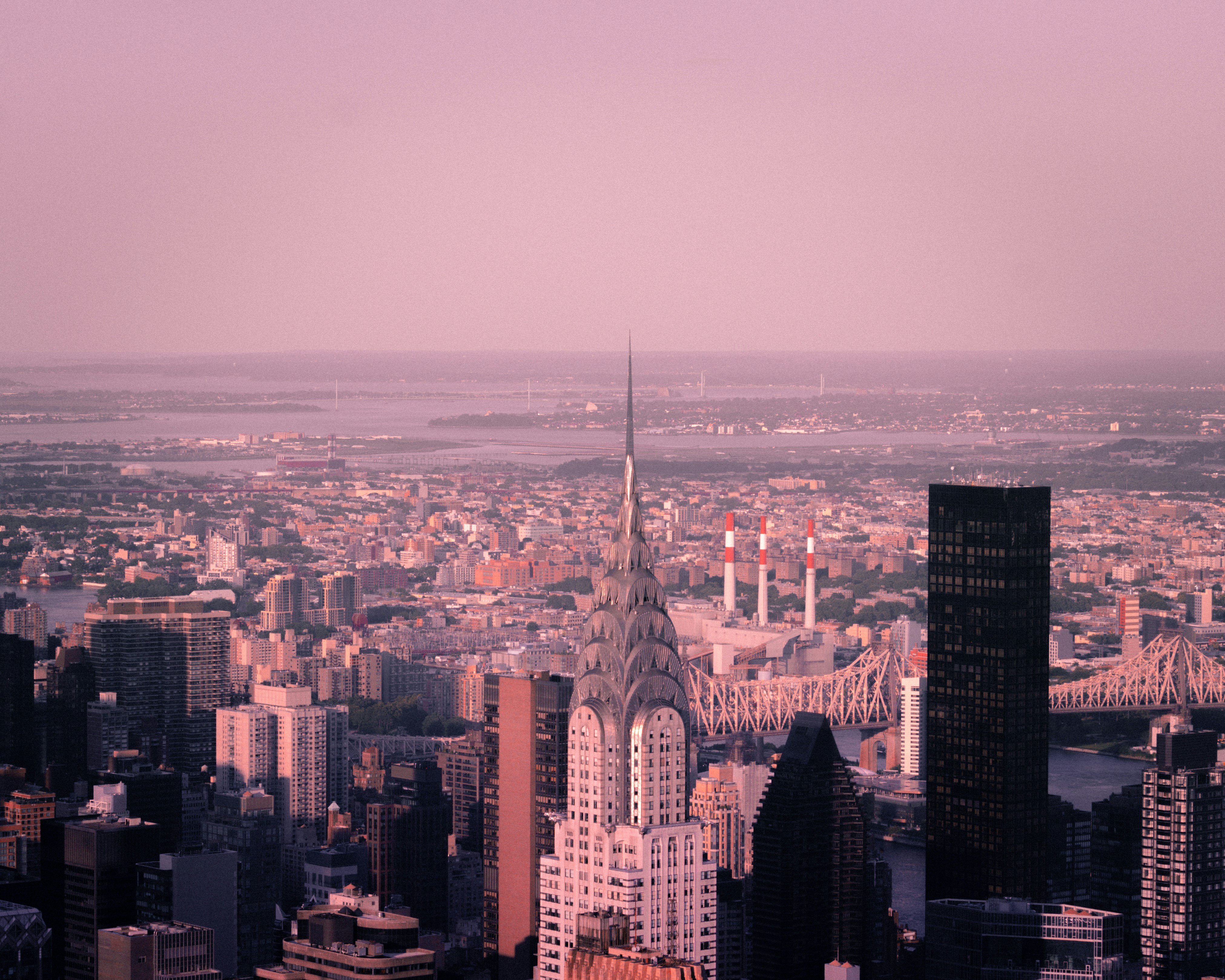 Chrysler Building piercing the pastel sky, surrounded by the sprawling cityscape of New York. The scene captures a blend of iconic architecture and urban expanse.