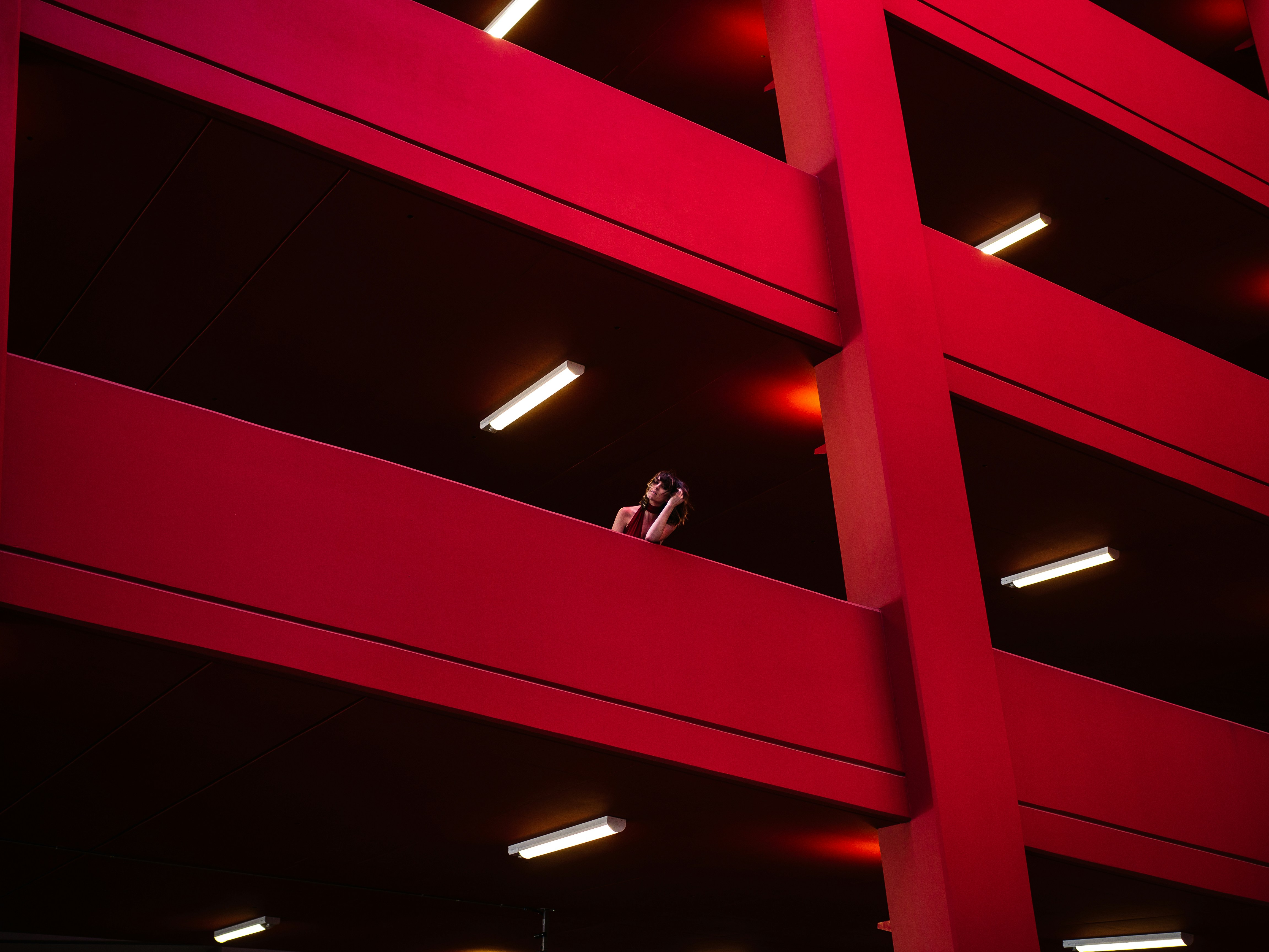 Crimson Atrium: A solitary observer on a red, multi-level parking structure