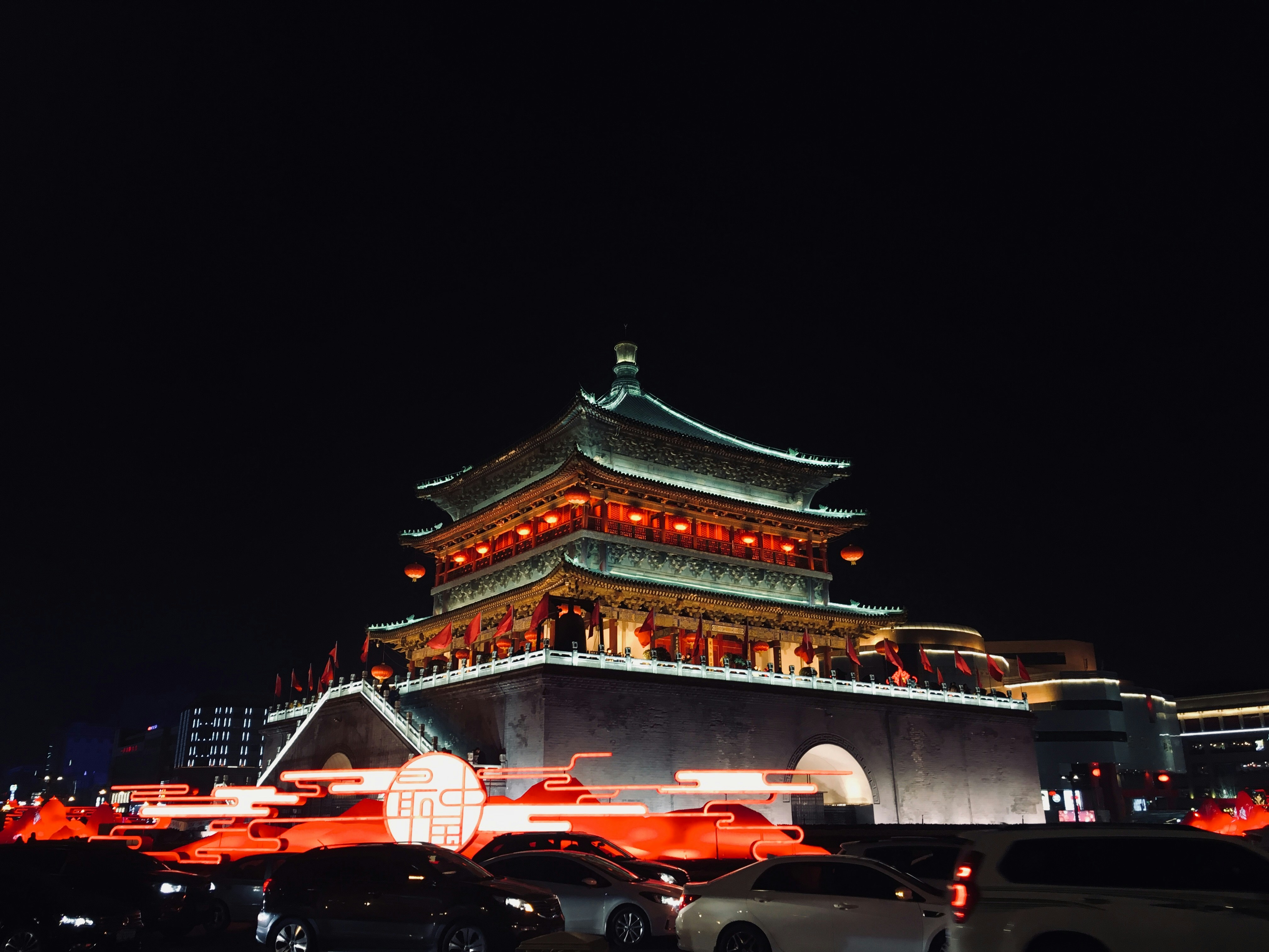 Red and white temple illuminated against a dark night sky with streaks of light from passing vehicles.
