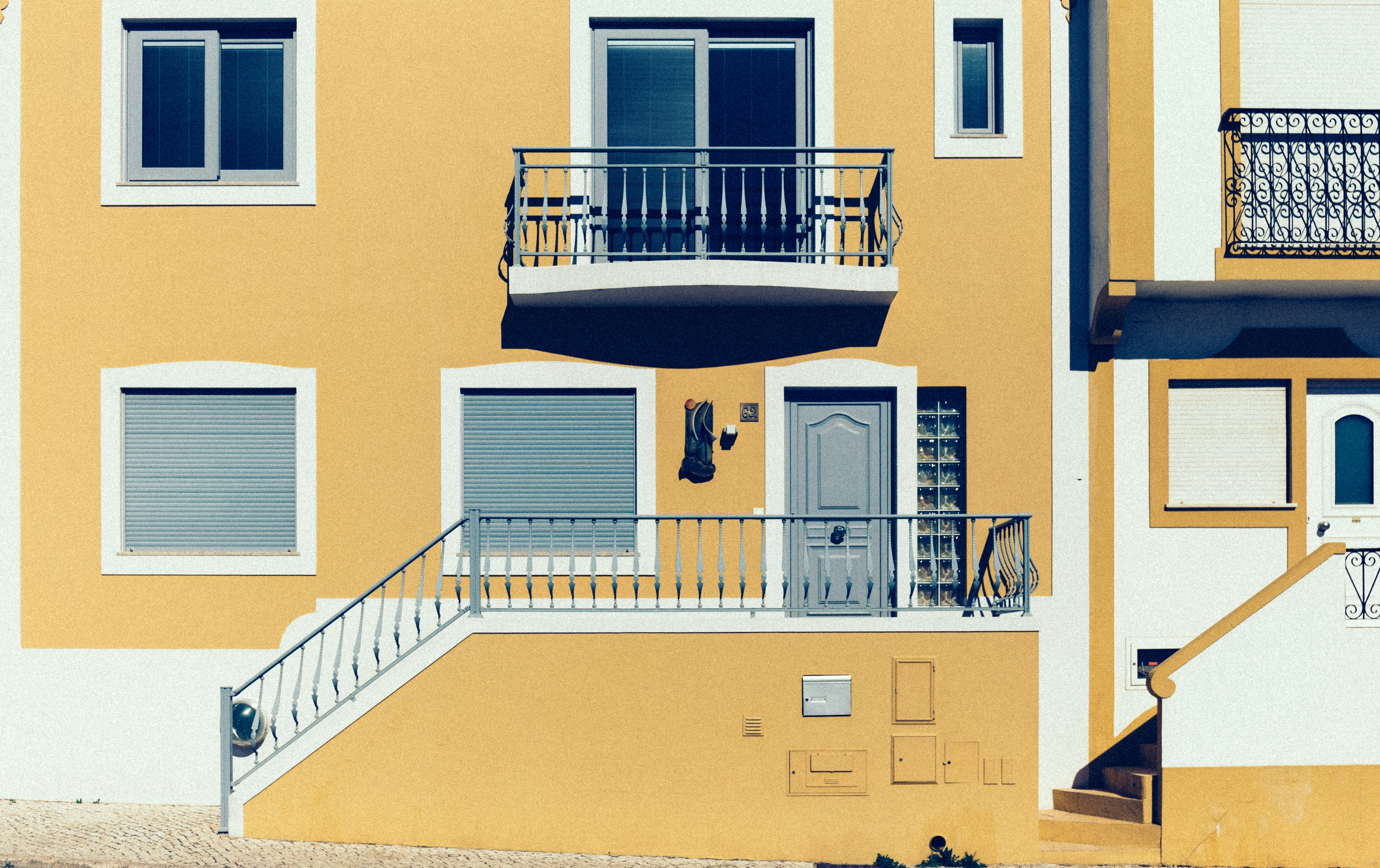 Bright yellow building with a balcony, featuring modern shutters and a decorative entrance. The design emphasizes clean lines and vibrant color.