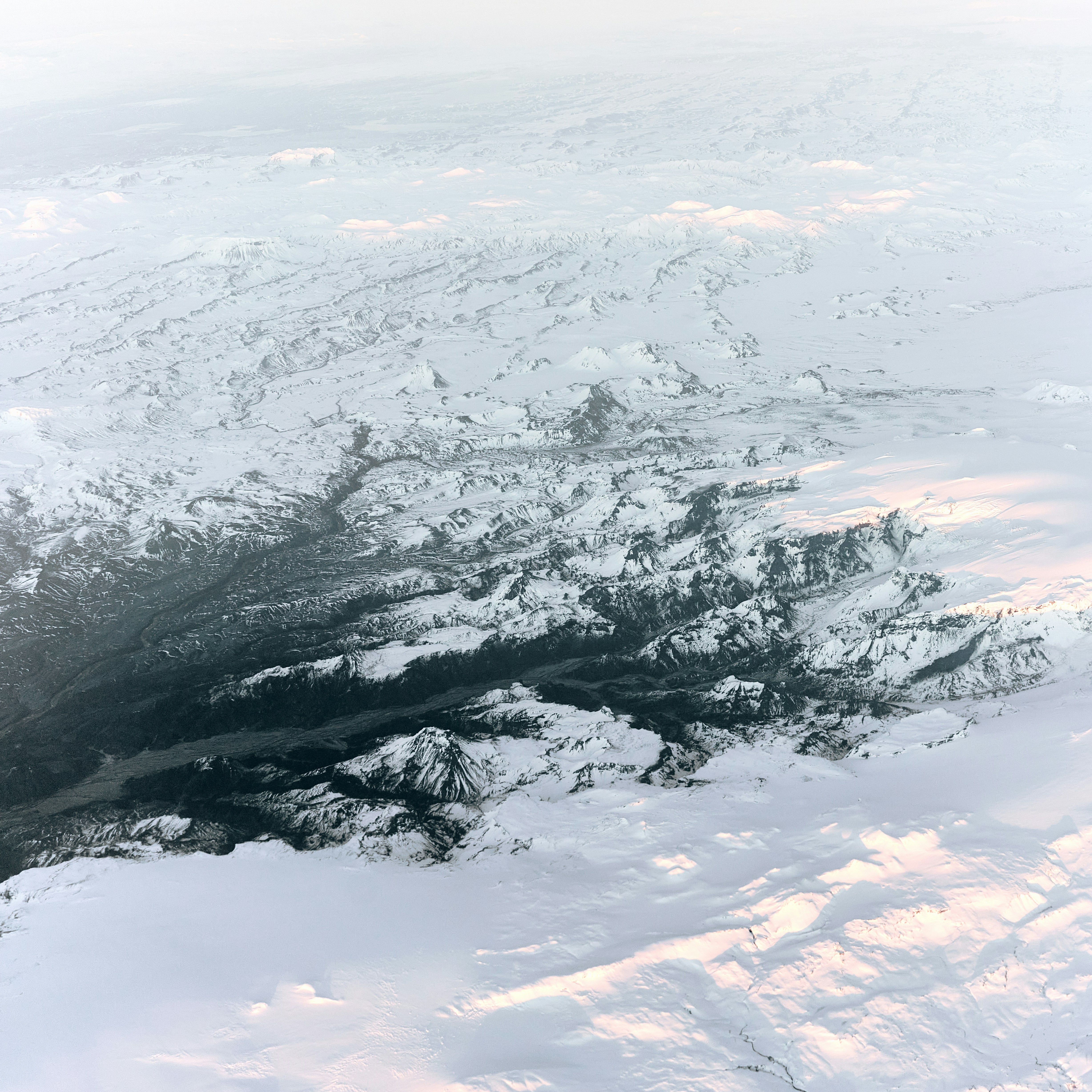 Aerial view showcasing vast snow-covered mountains and valleys, revealing the intricate patterns of glacial formations and rugged terrain.