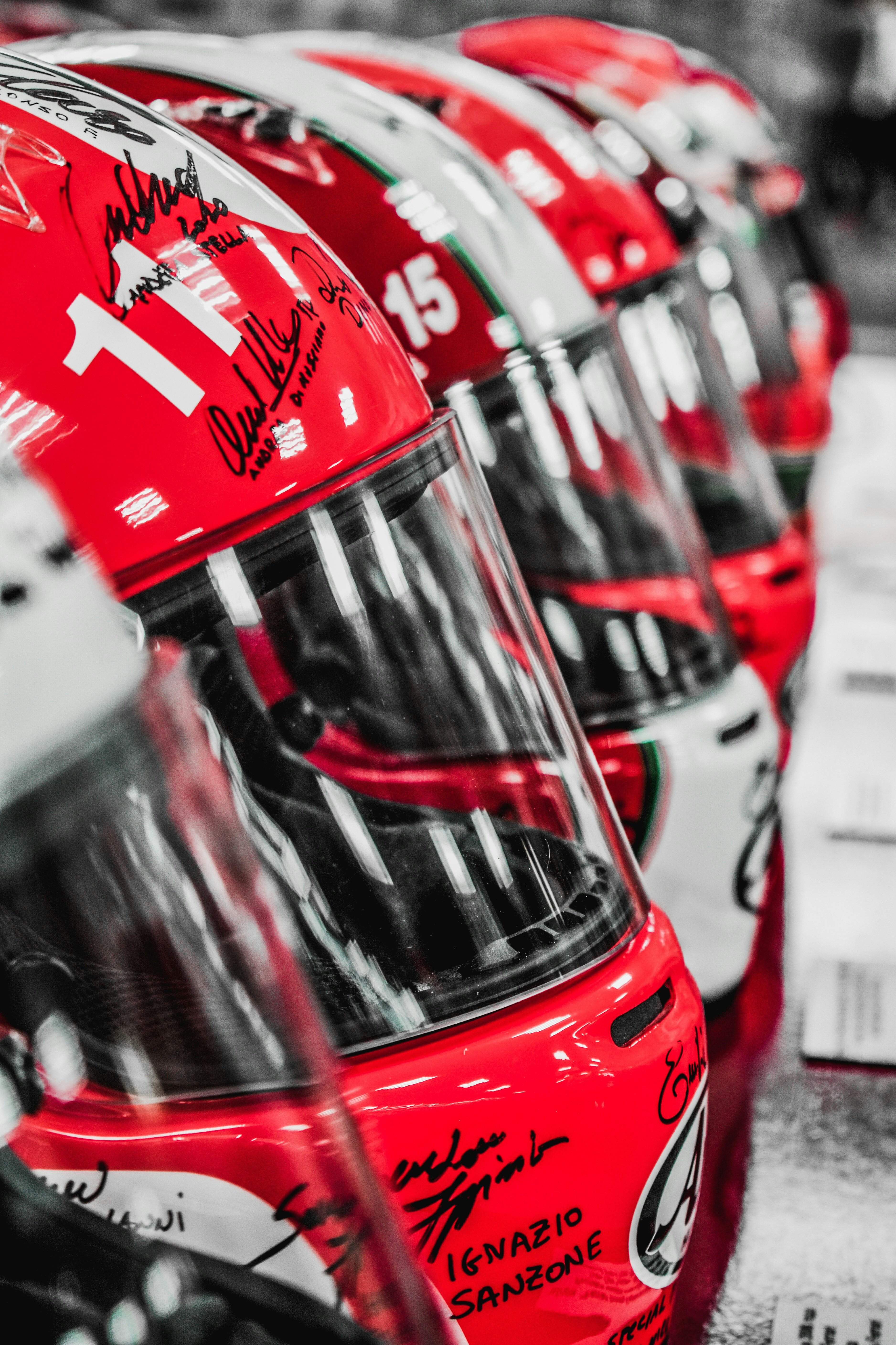A collection of signed racing helmets arranged in a row, showcasing their vibrant red colors and unique designs. The helmets reflect a rich history of motorsport.