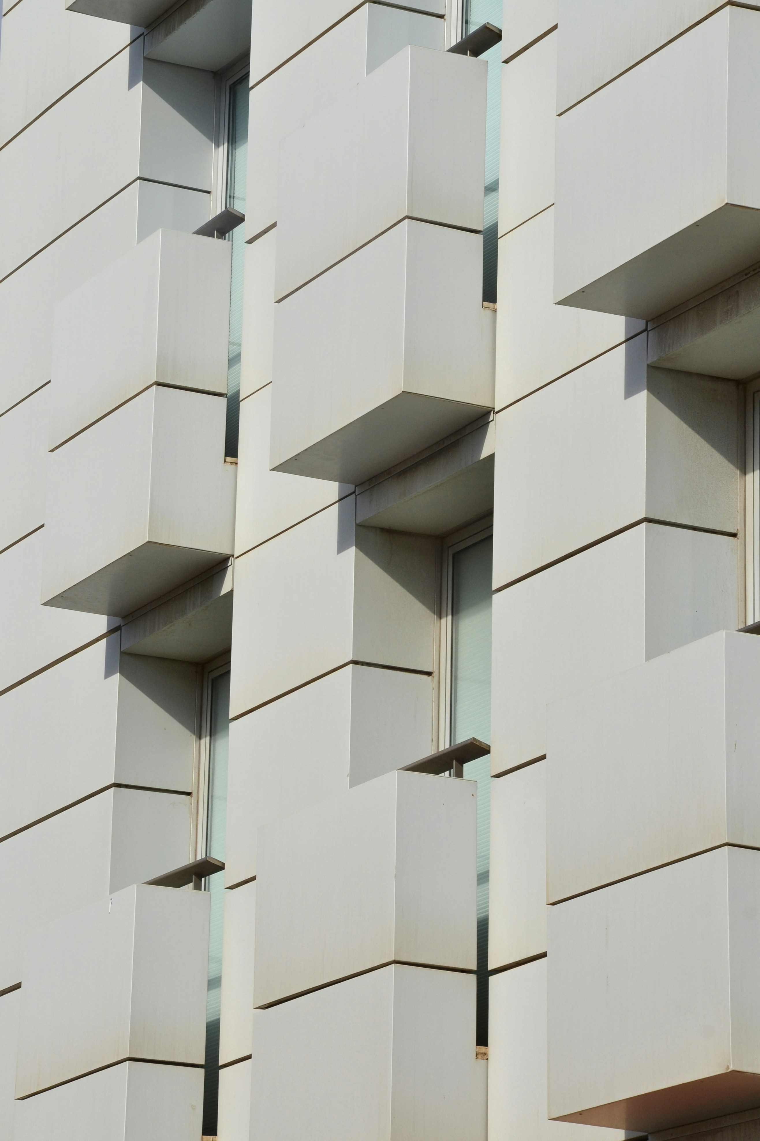 Abstract view of a contemporary building facade featuring protruding geometric shapes and windows. The design emphasizes clean lines and a minimalist aesthetic.