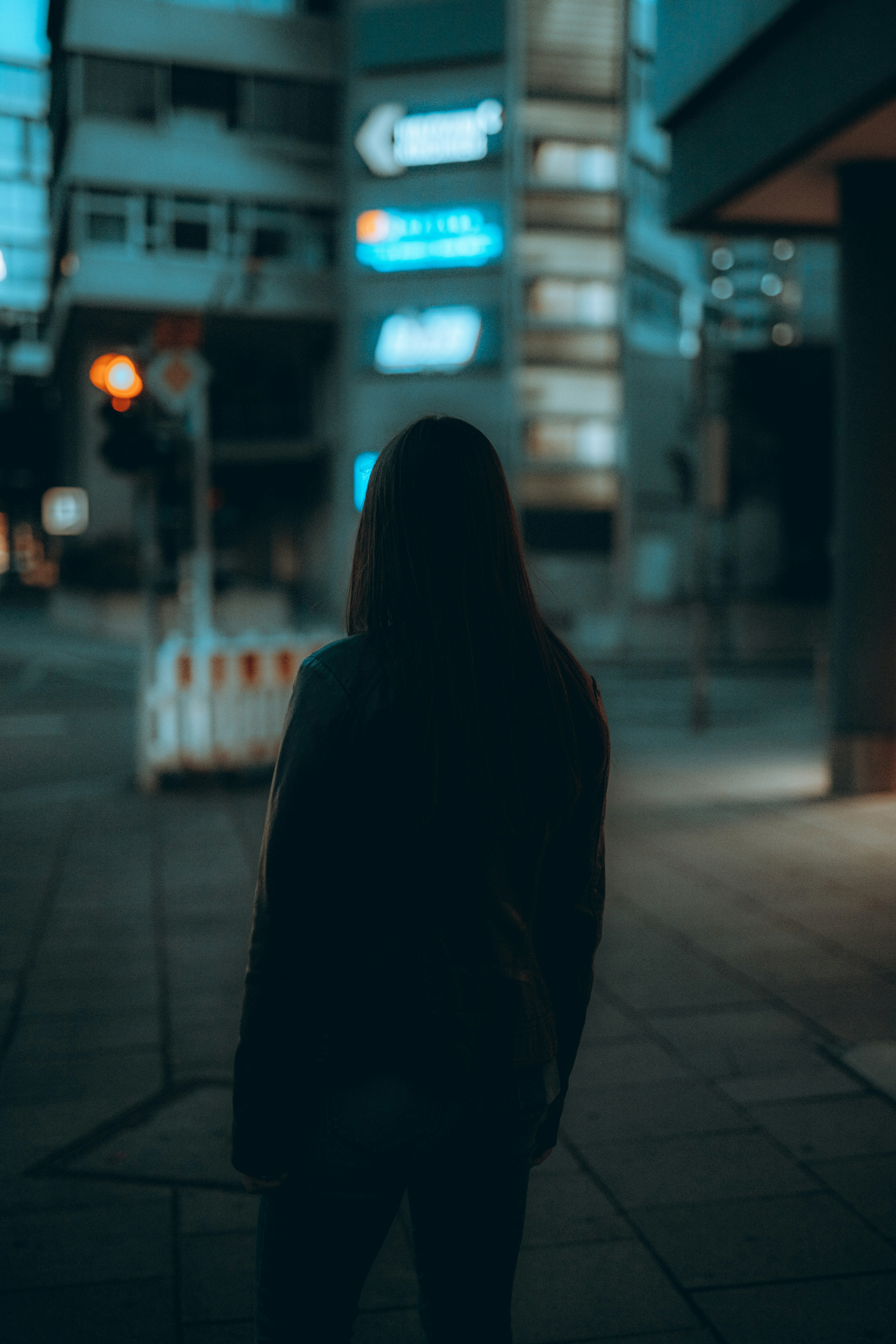 Silhouette of a woman standing in an urban setting, illuminated by neon signs and streetlights. The scene captures the essence of city life after dark.