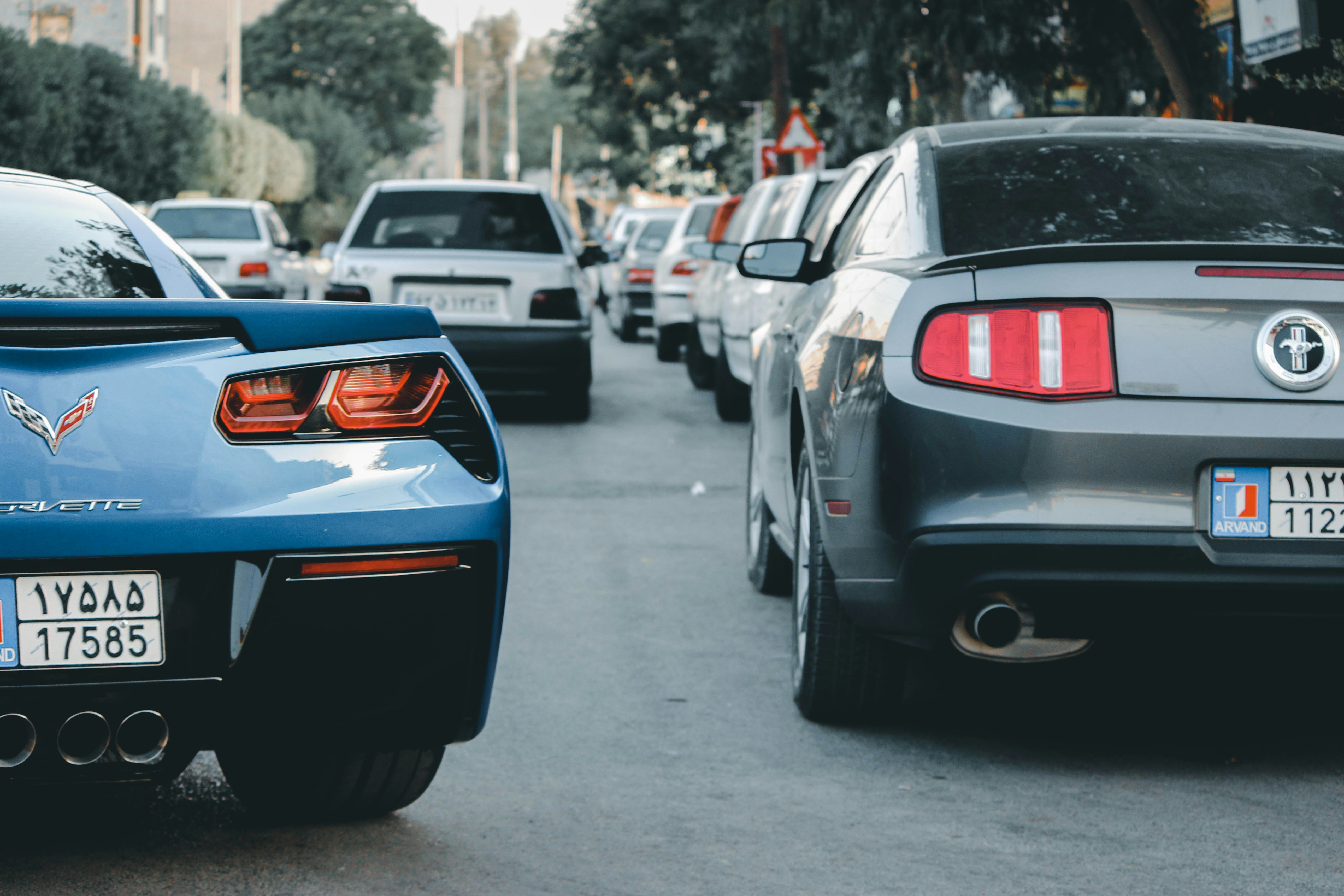 Blue Chevrolet Corvette C7 Stingray and gray Ford Mustang parked on a busy city street in traffic.
