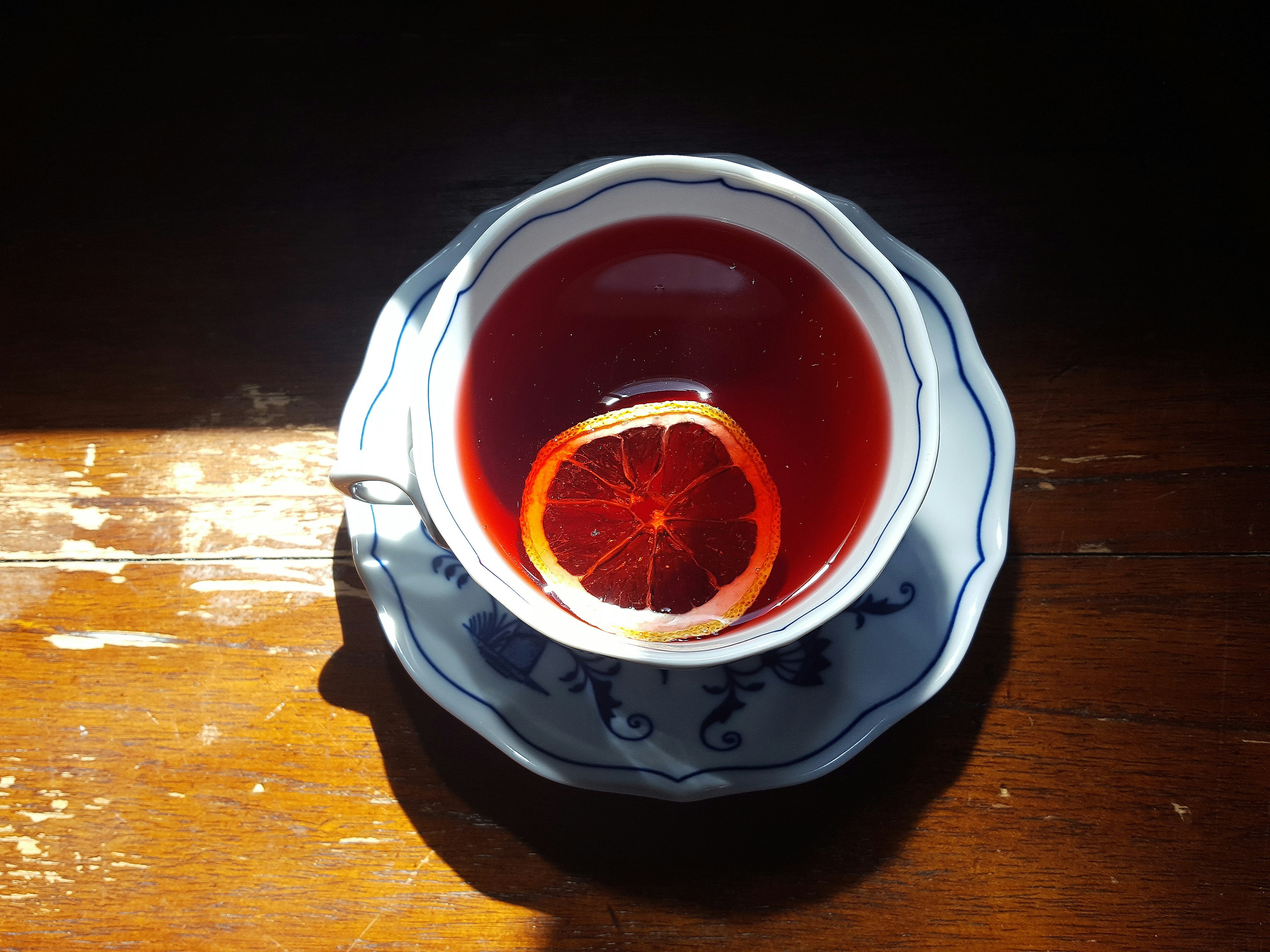 Cup of red tea with a slice of lemon resting on a delicate saucer, illuminated by soft sunlight on a wooden table.