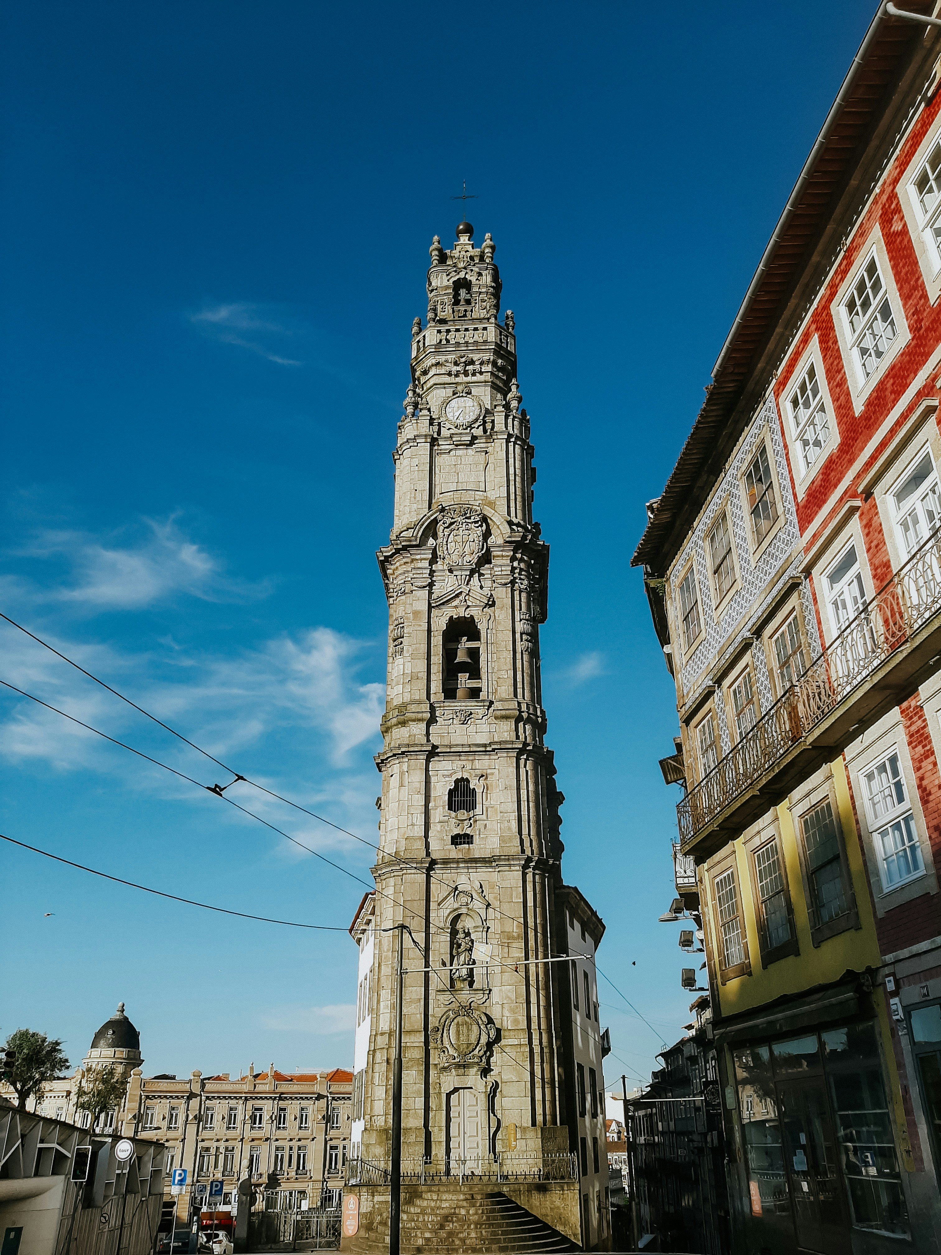 Historic clock tower rising majestically against a clear blue sky, flanked by colorful buildings in a bustling urban setting.