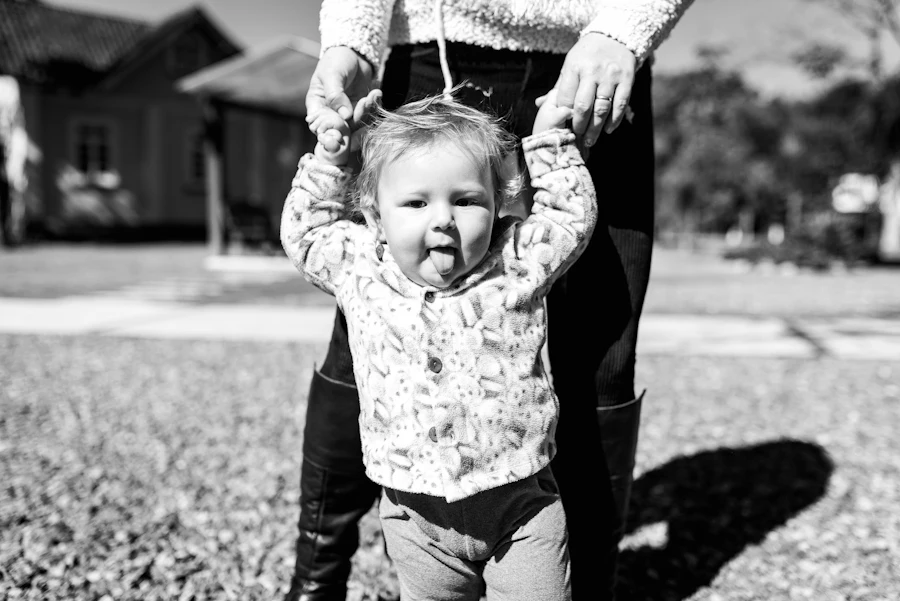 A toddler playfully sticking out their tongue while being held by an adult, set against a blurred background of a sunny day. The image captures a moment of carefree joy.