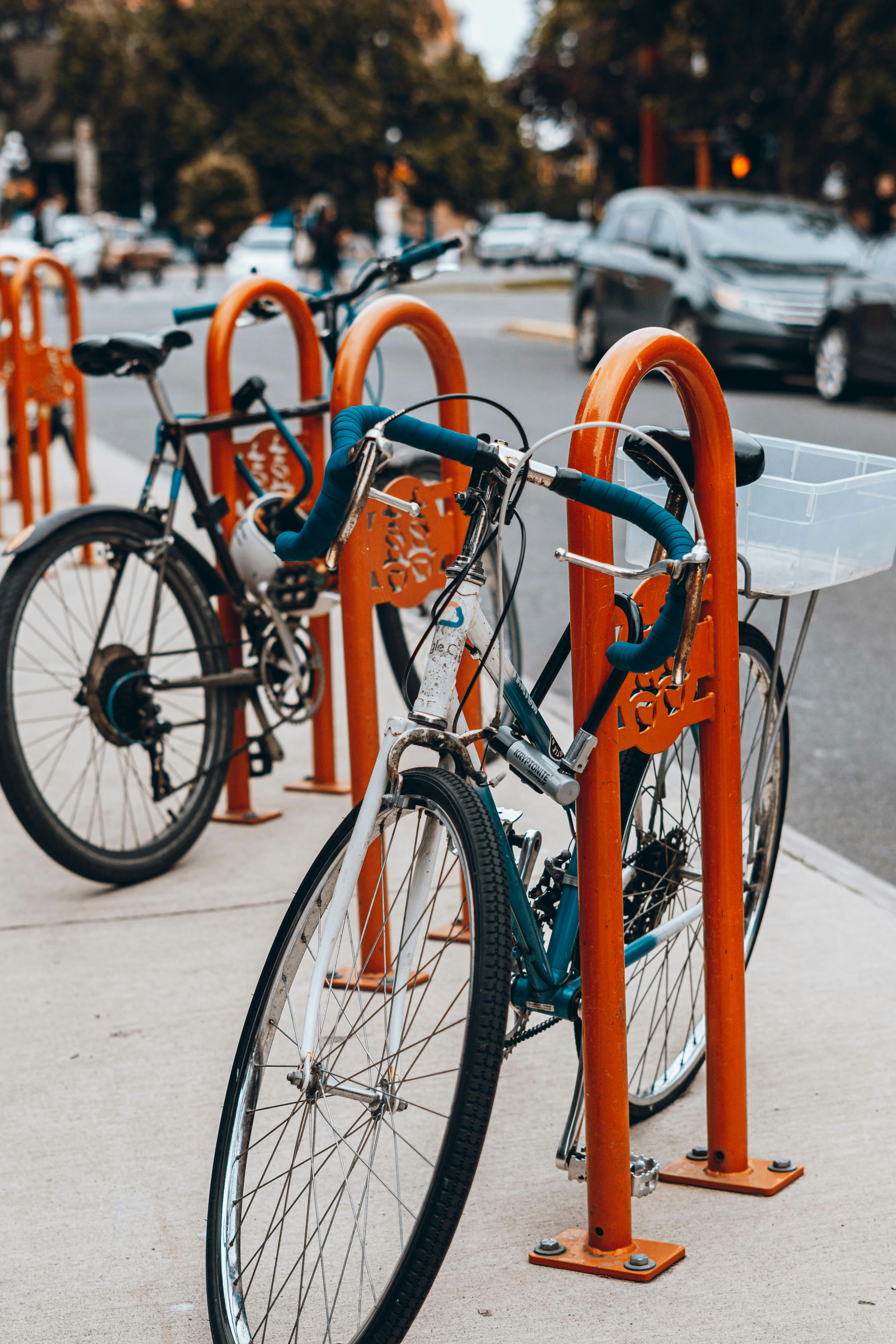 Two bicycles secured to vibrant orange bike racks on a bustling city street, showcasing urban life and transportation options.