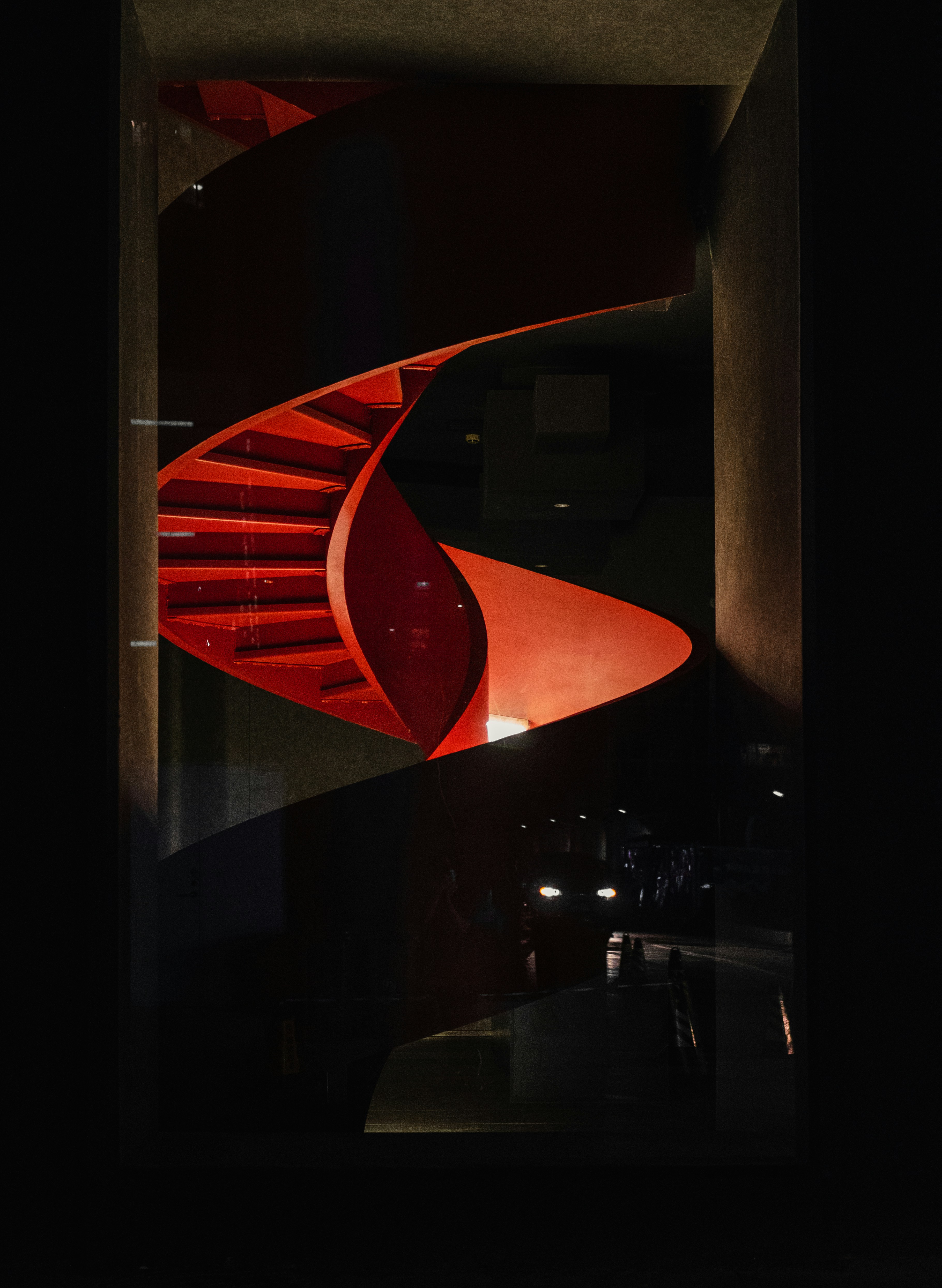 A vibrant red spiral staircase illuminated against a dark backdrop, showcasing architectural elegance and dynamic lines.
