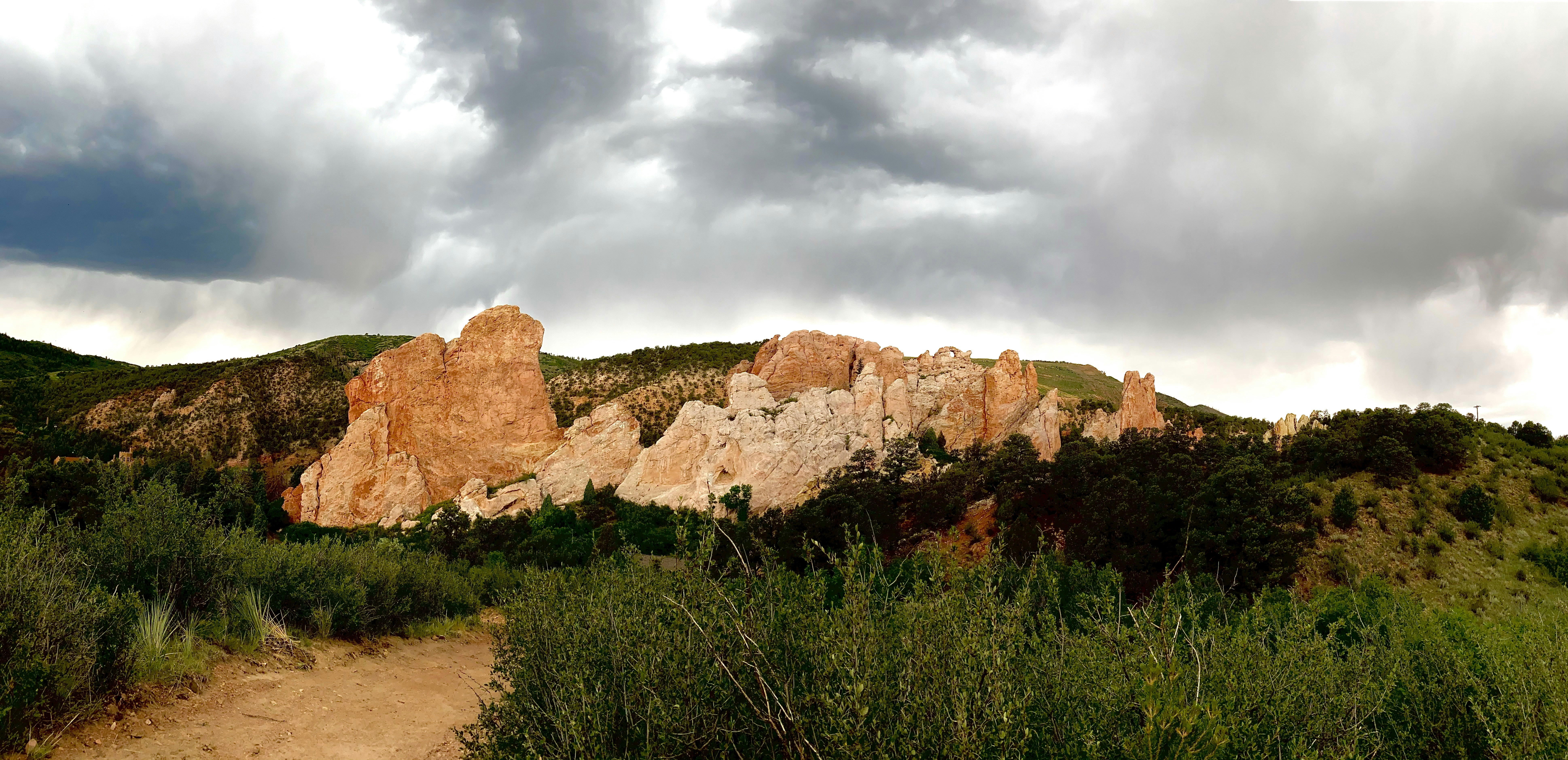 A panoramic view of rugged, weathered cliffs surrounded by lush greenery under a dramatic sky.