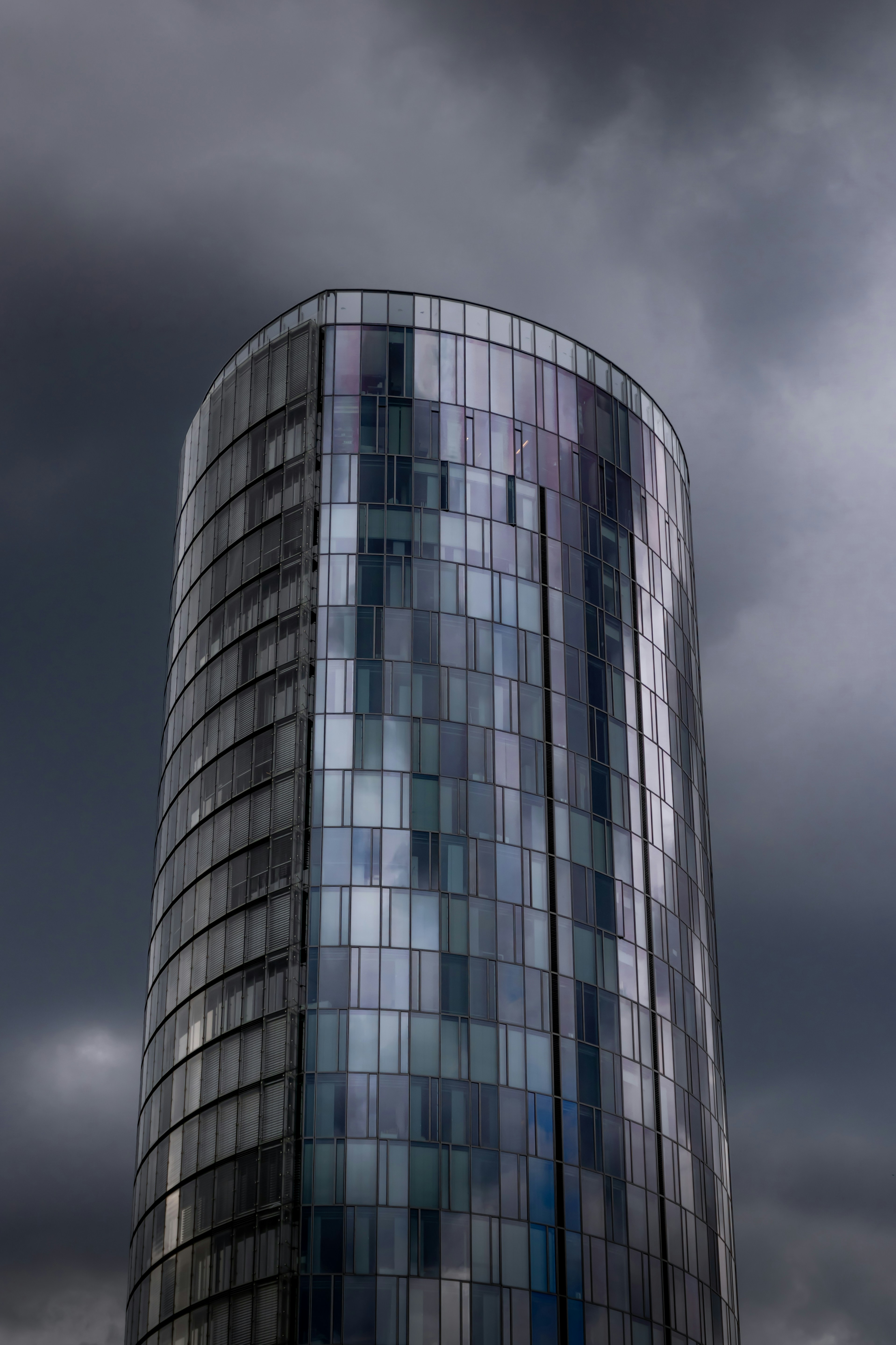 Sleek, reflective skyscraper against a dramatic, overcast sky, showcasing contemporary architecture and urban design.