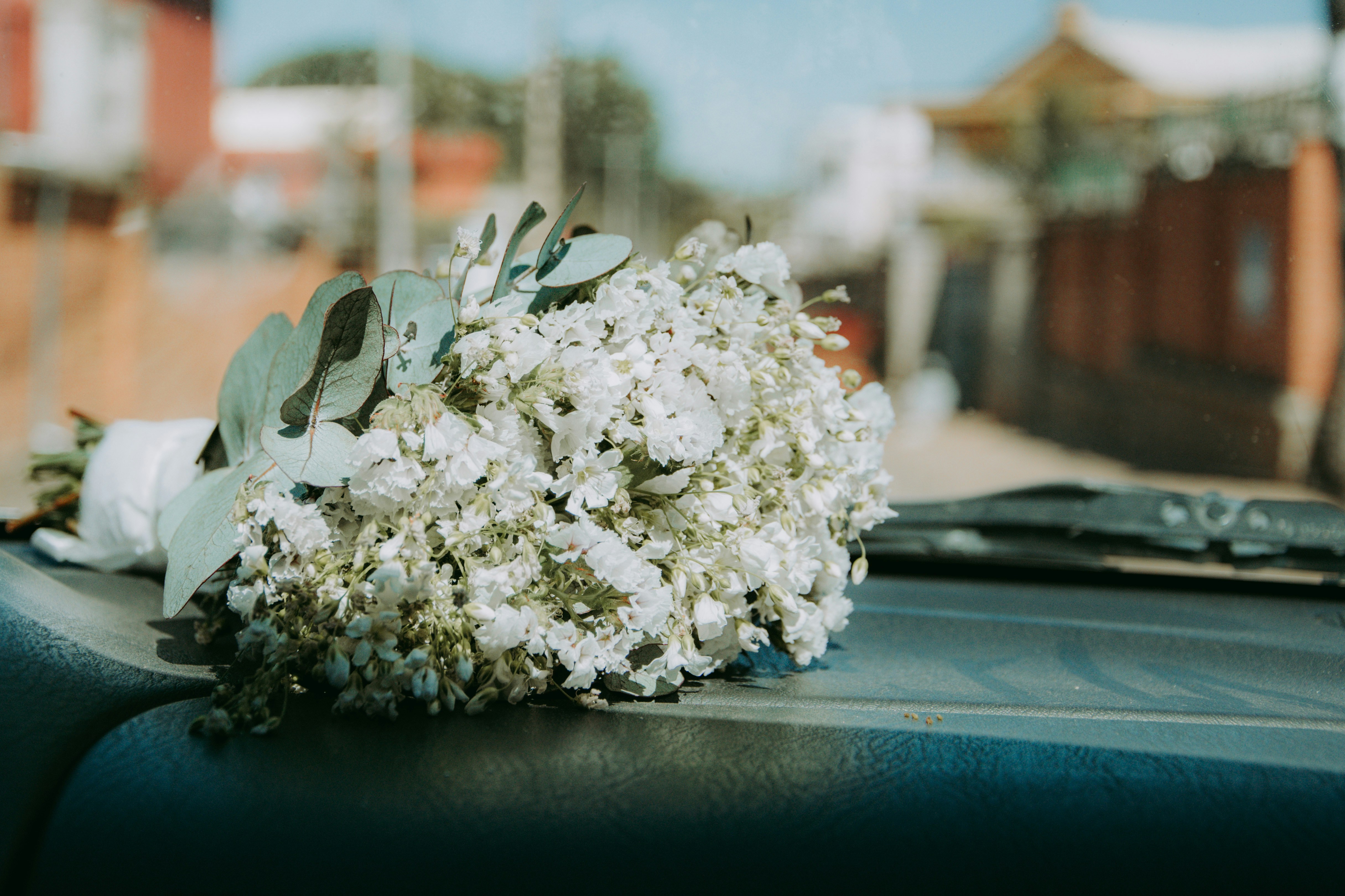 Delicate bouquet of white flowers and greenery resting on a car dashboard, capturing a moment of tranquility amidst a bustling environment.