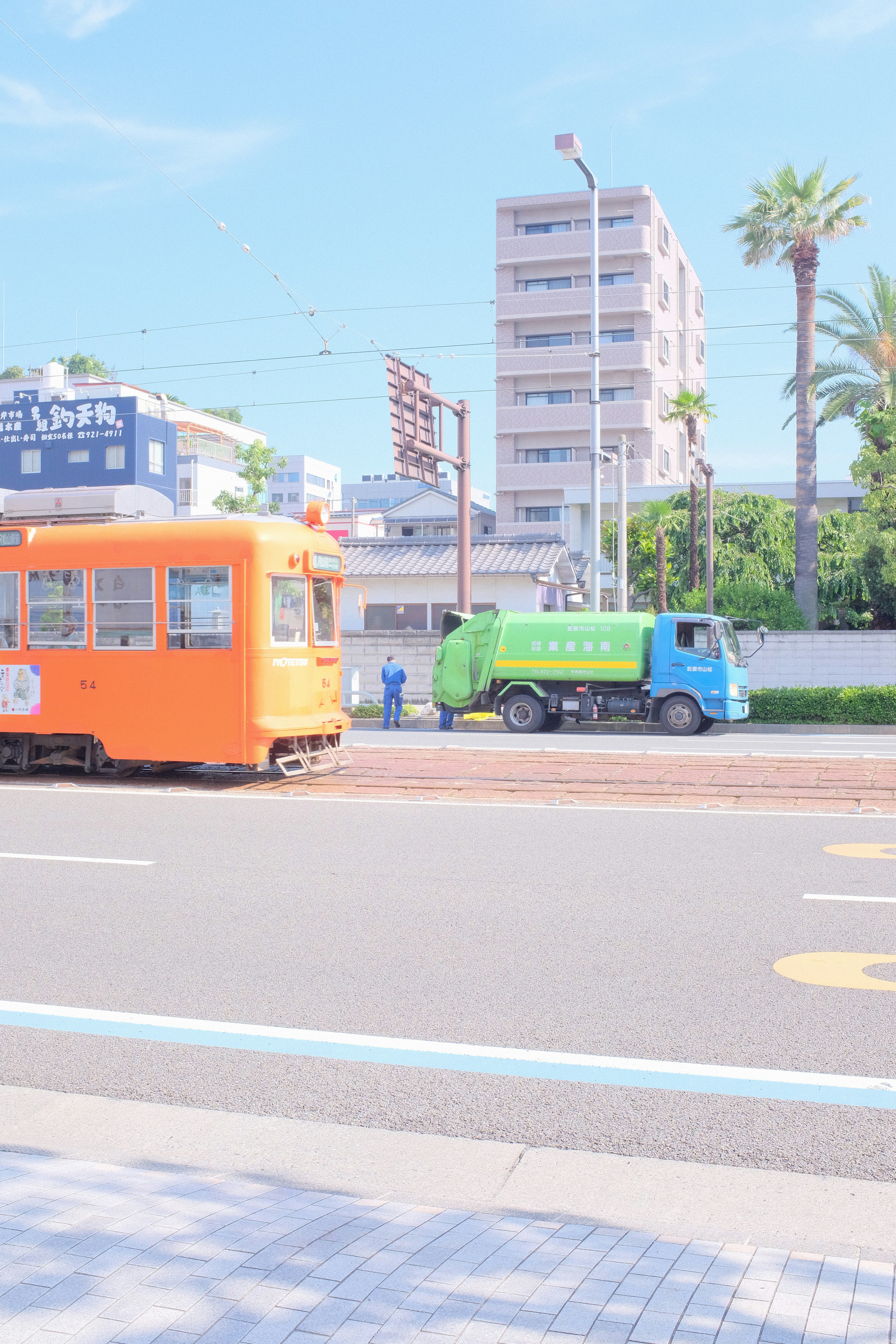 An orange tram alongside a green garbage truck in a vibrant cityscape, showcasing the daily rhythm of urban life.