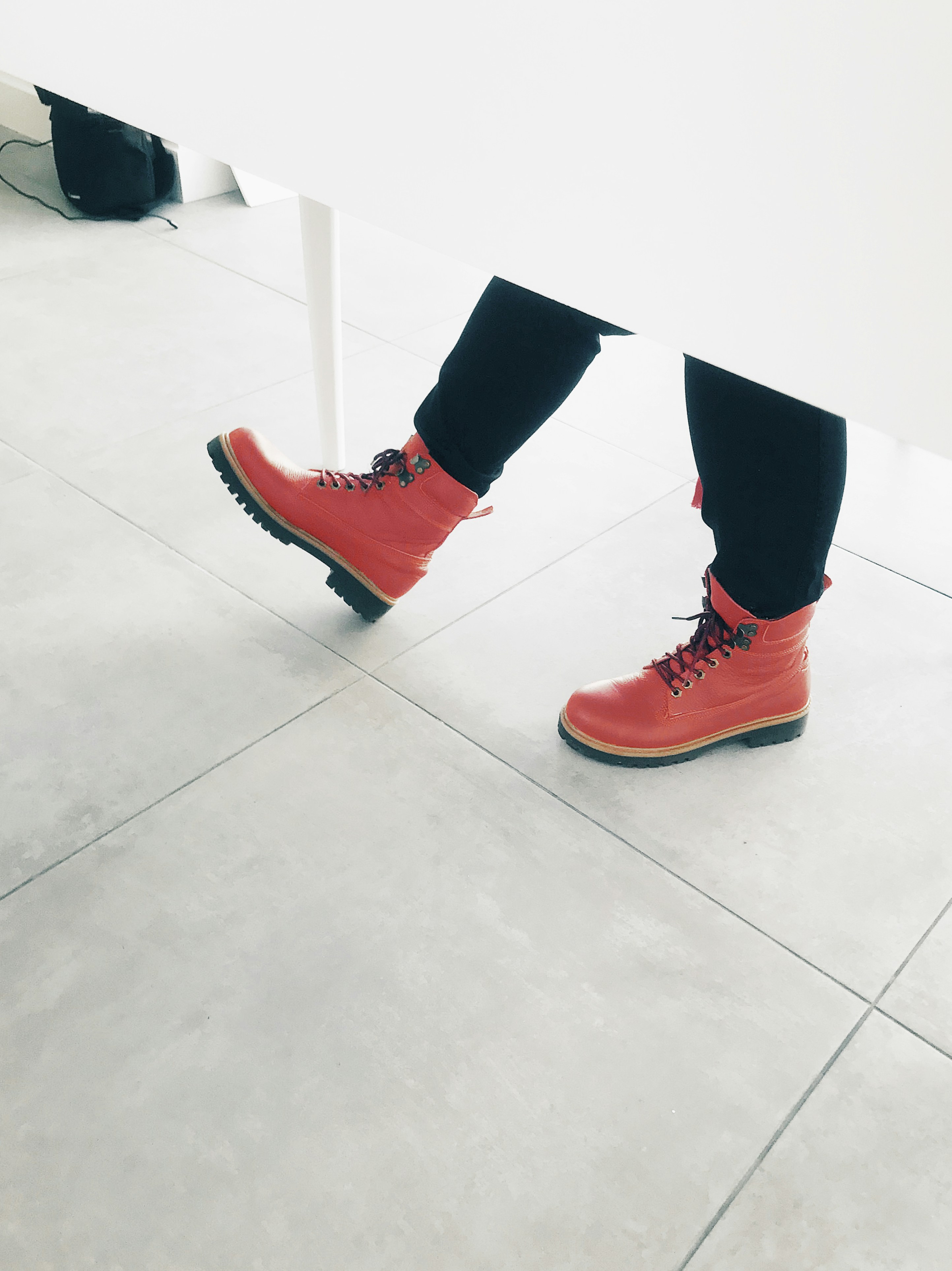 Bright red boots peeking out from under a white table in a modern, minimalist setting.