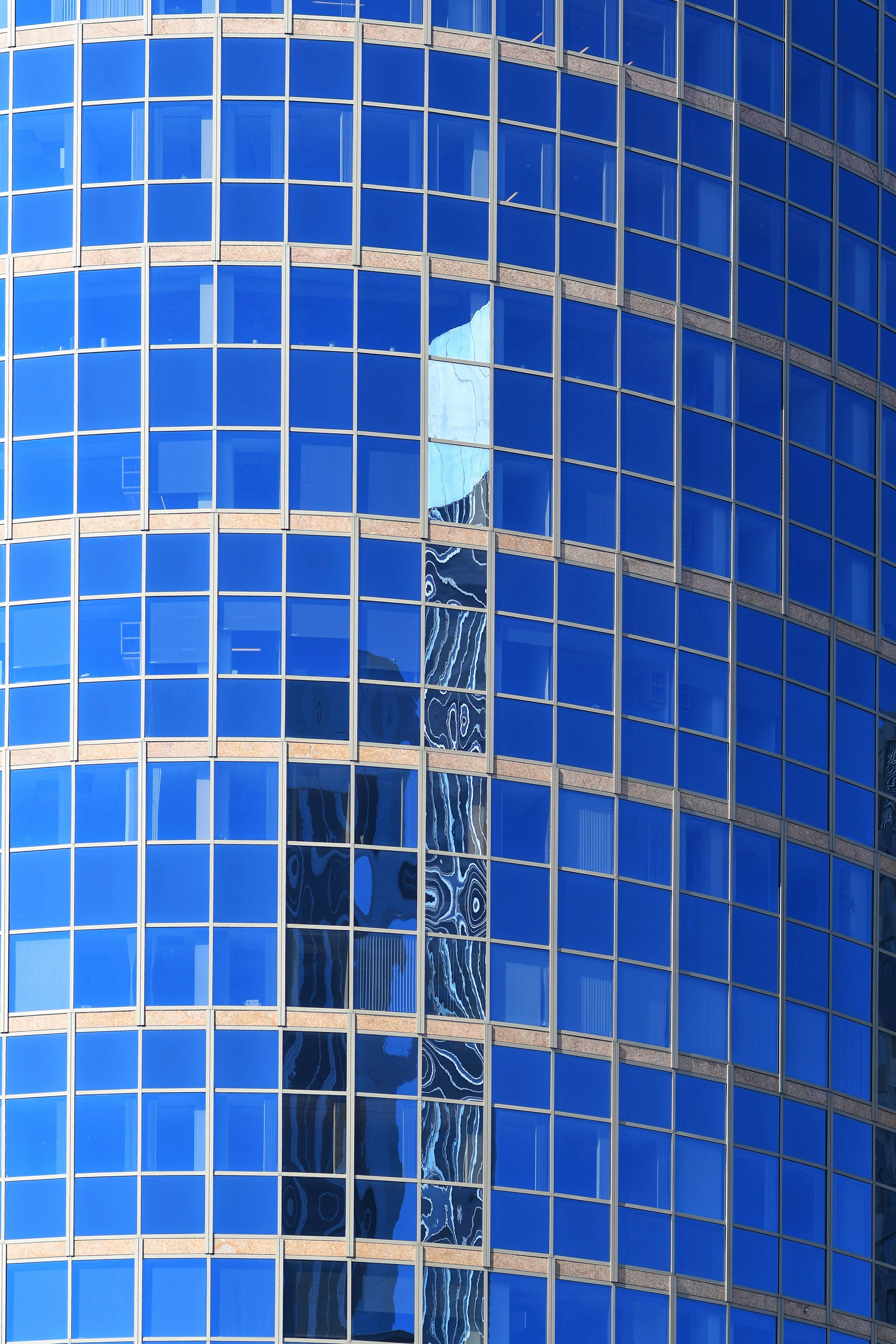 Modern skyscraper windows reflecting surrounding architecture and the sky, showcasing a blend of geometric patterns and vibrant colors.
