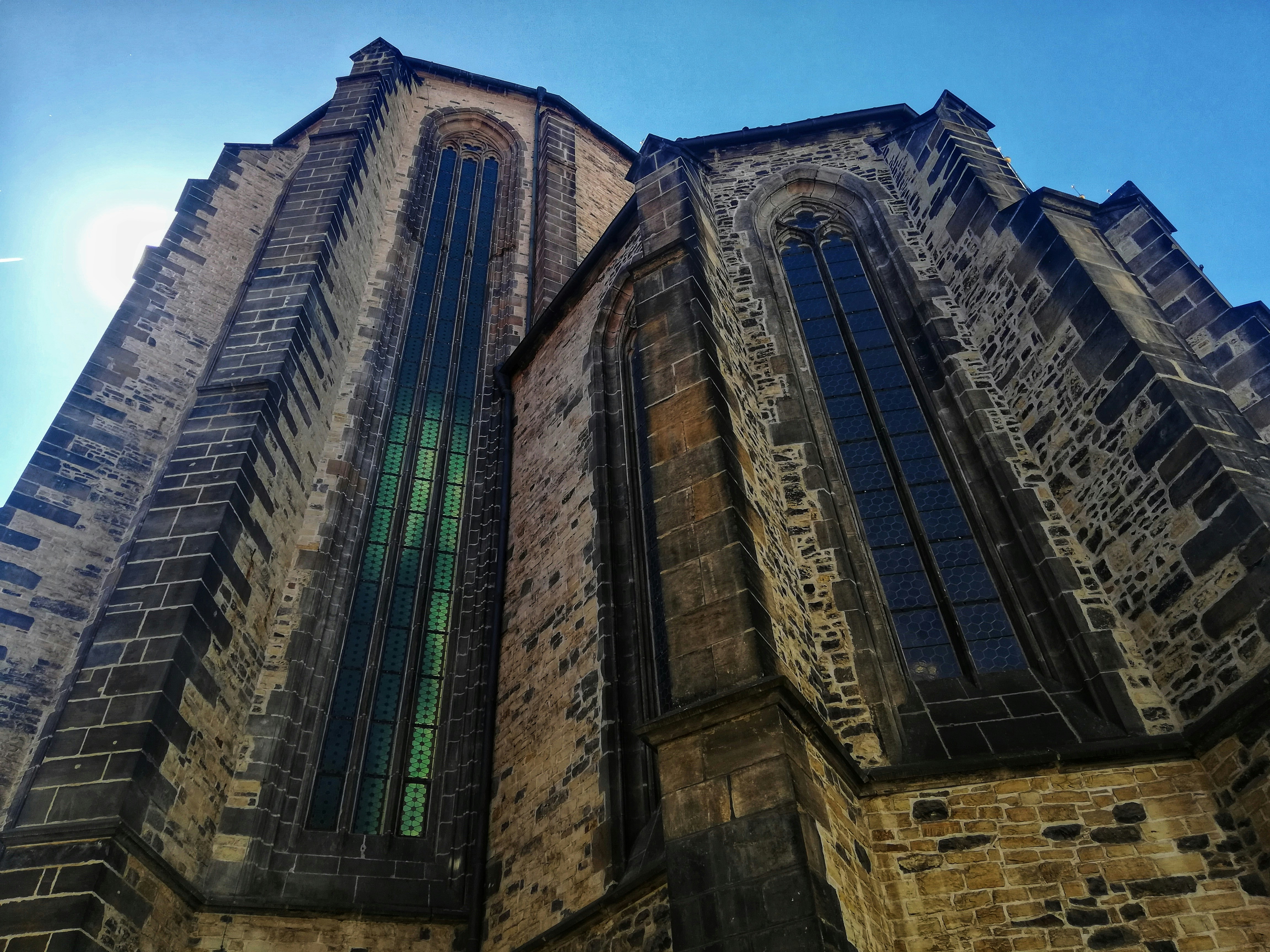 Low-angle view of a Gothic cathedral facade with tall, narrow windows and weathered stone against a bright blue sky.