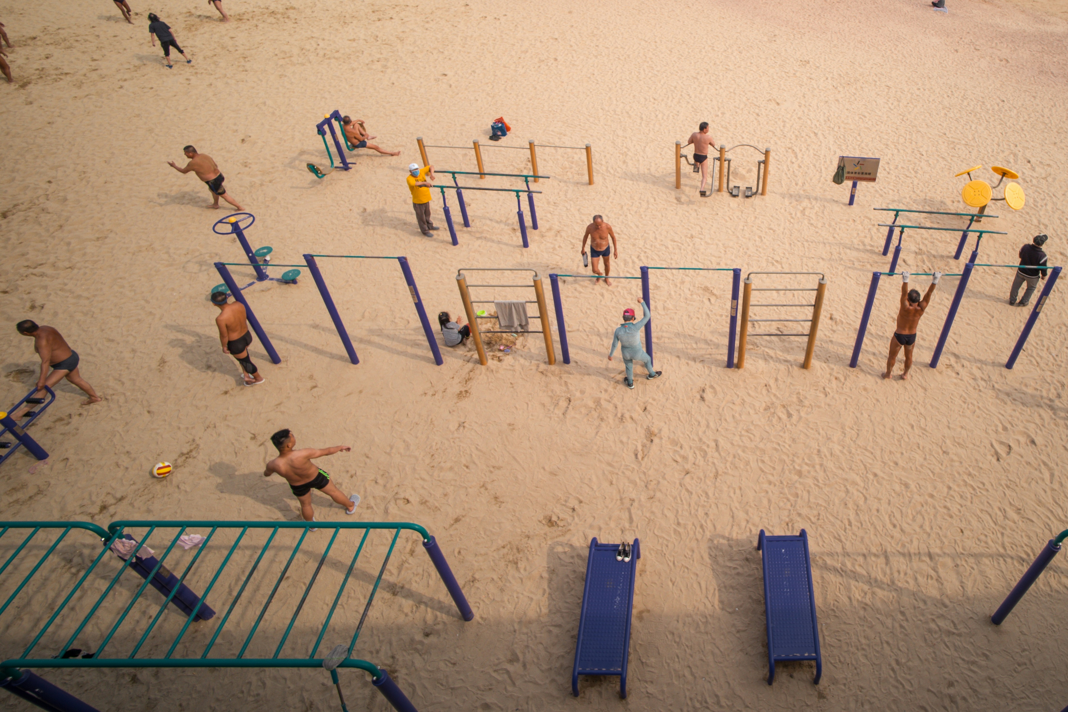 Outdoor gym scene on a sandy beach with individuals engaged in various exercises, showcasing a vibrant community atmosphere.