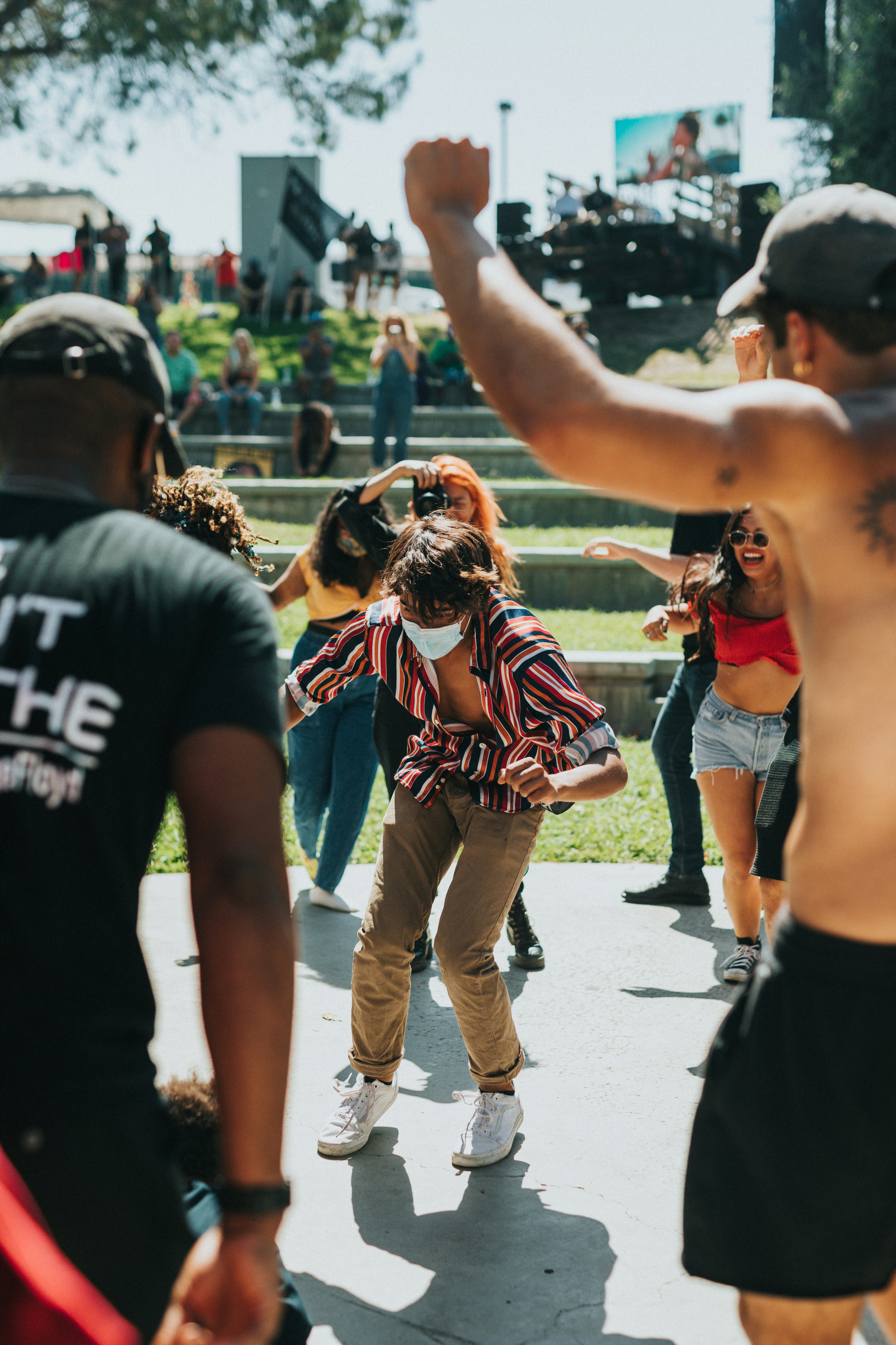 Energetic group of dancers enjoying a lively outdoor event under the sun, showcasing diverse expressions of movement and camaraderie.