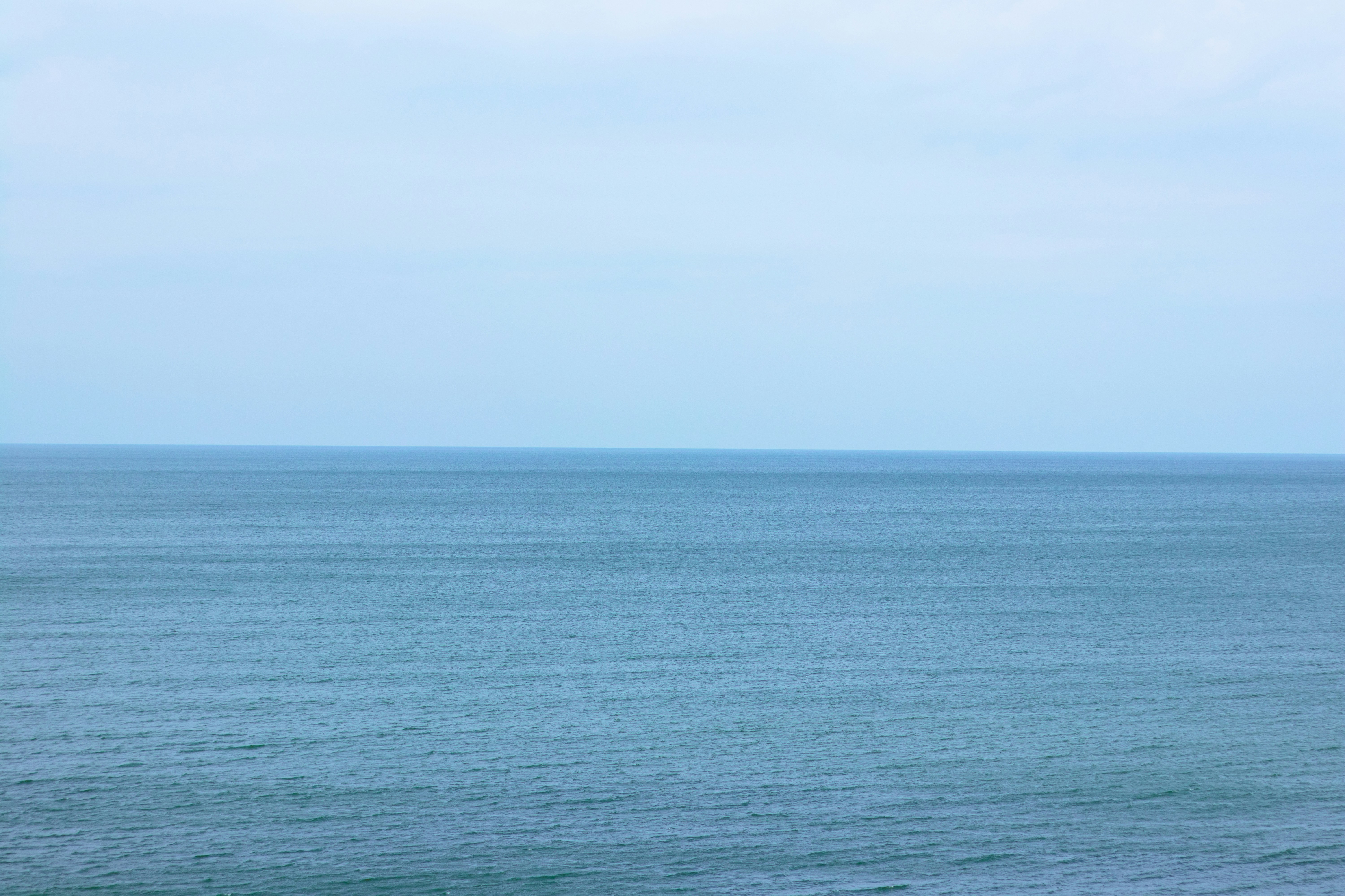 Calm sea stretching to the horizon under a soft blue sky, capturing the serene essence of nature's vastness.
