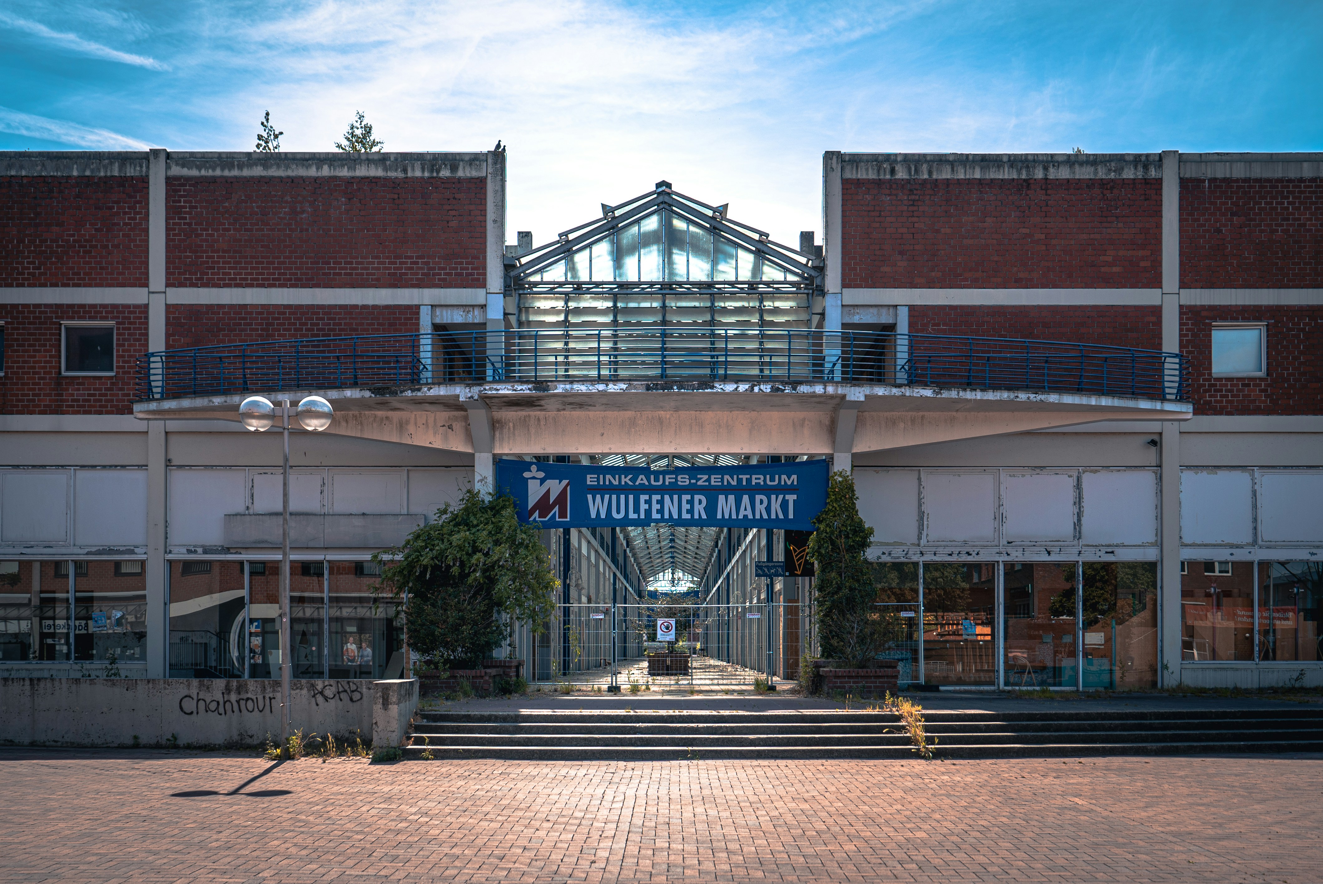 Facade of the abandoned Wulfener Markt with overgrown plants and a faded sign under a blue sky.
