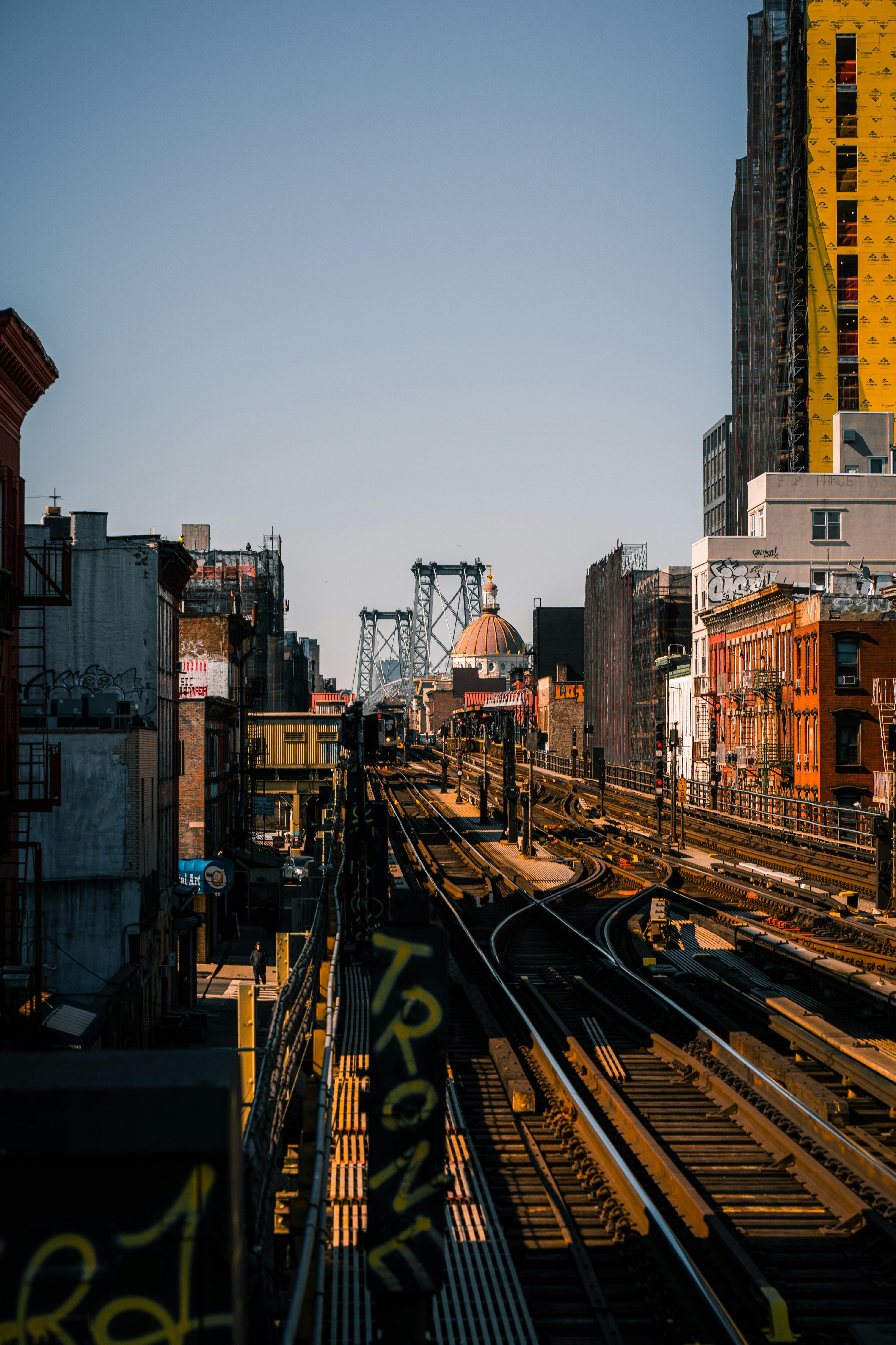 Elevated view of train tracks weaving through a vibrant urban landscape, framed by buildings and a distant bridge. The scene captures the essence of city life.