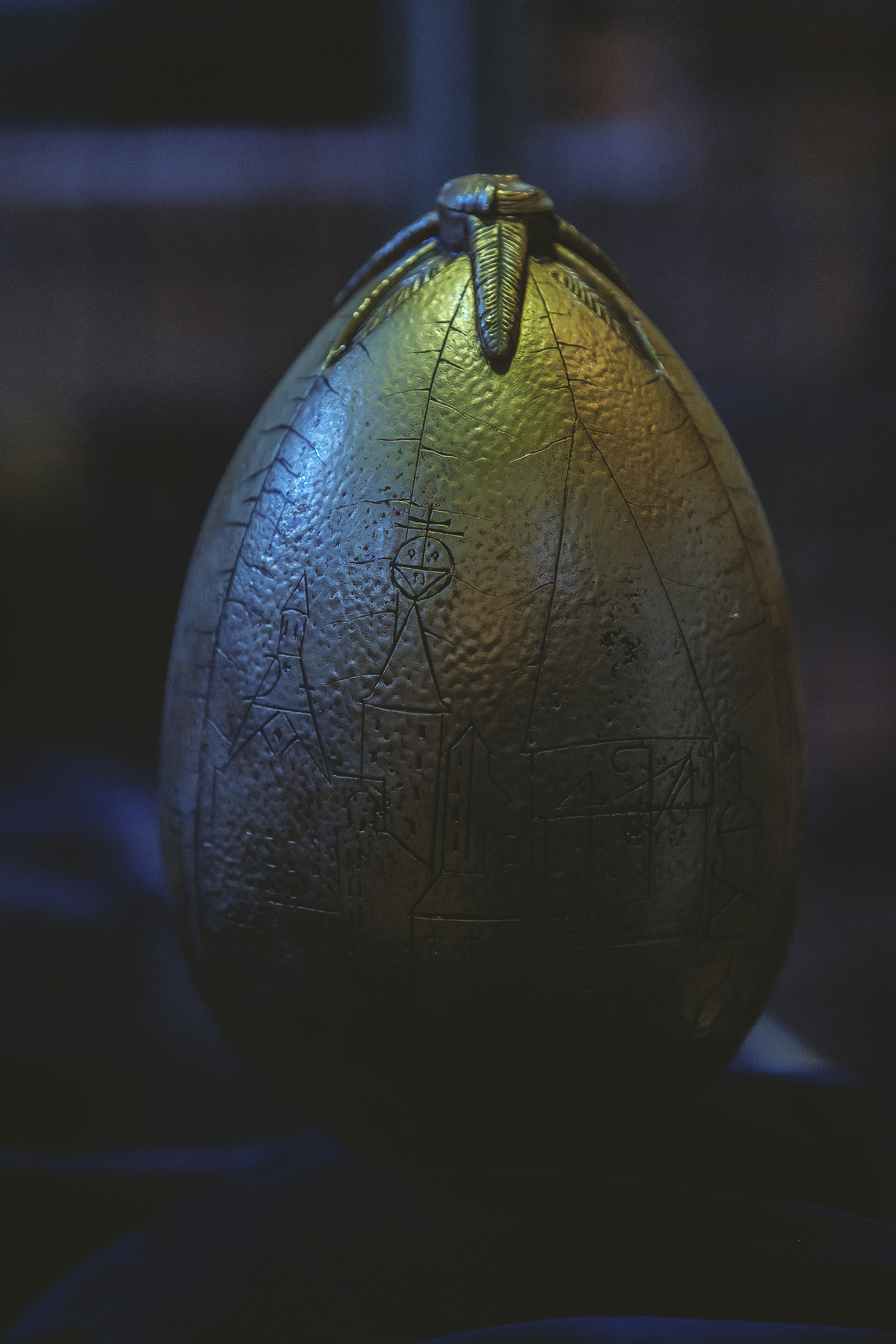 Intricately designed golden egg-shaped artifact with engraved architectural motifs, illuminated in a soft glow.