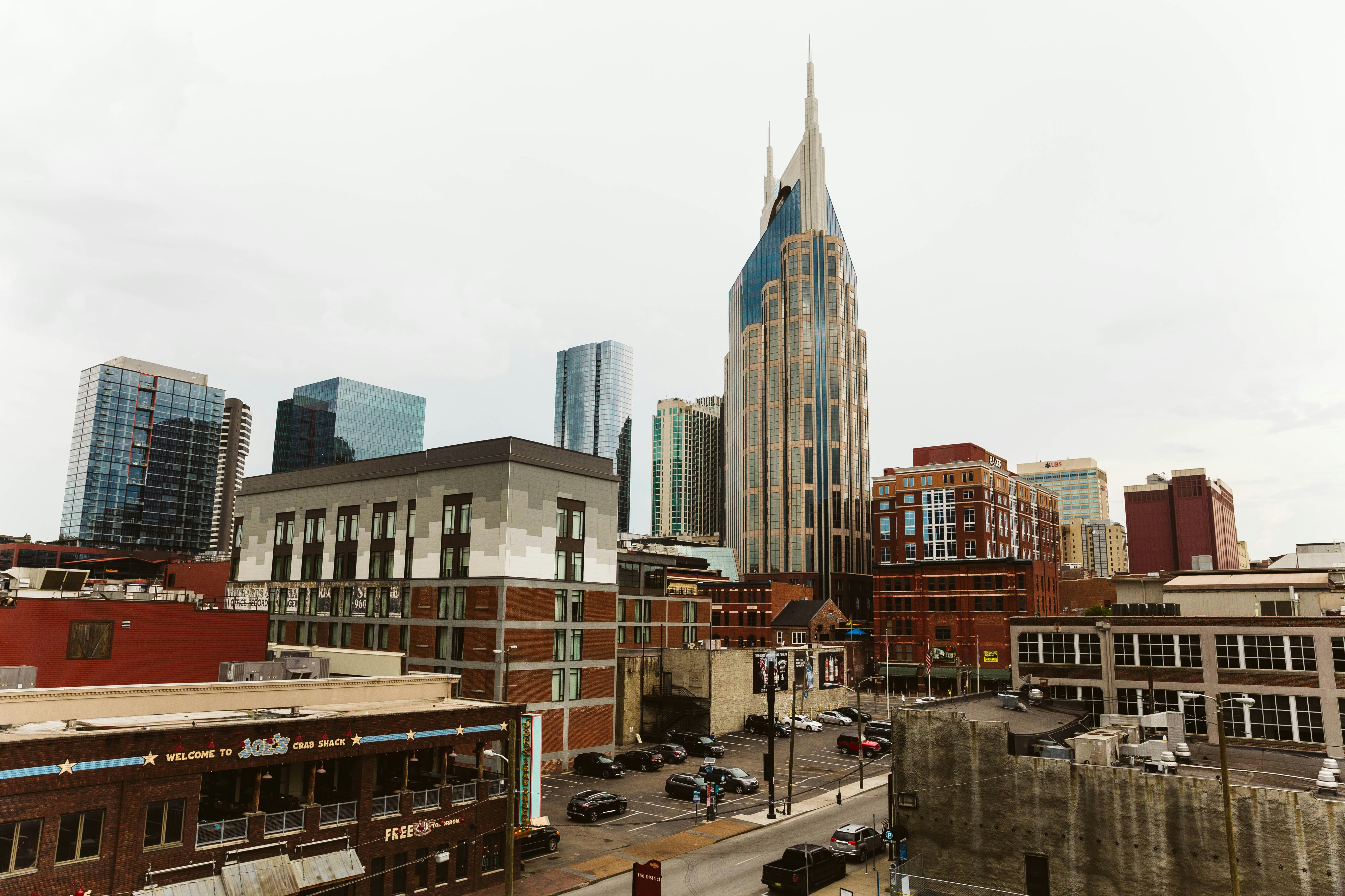 High-rise buildings and parked cars line a bustling city street under a cloudy sky.