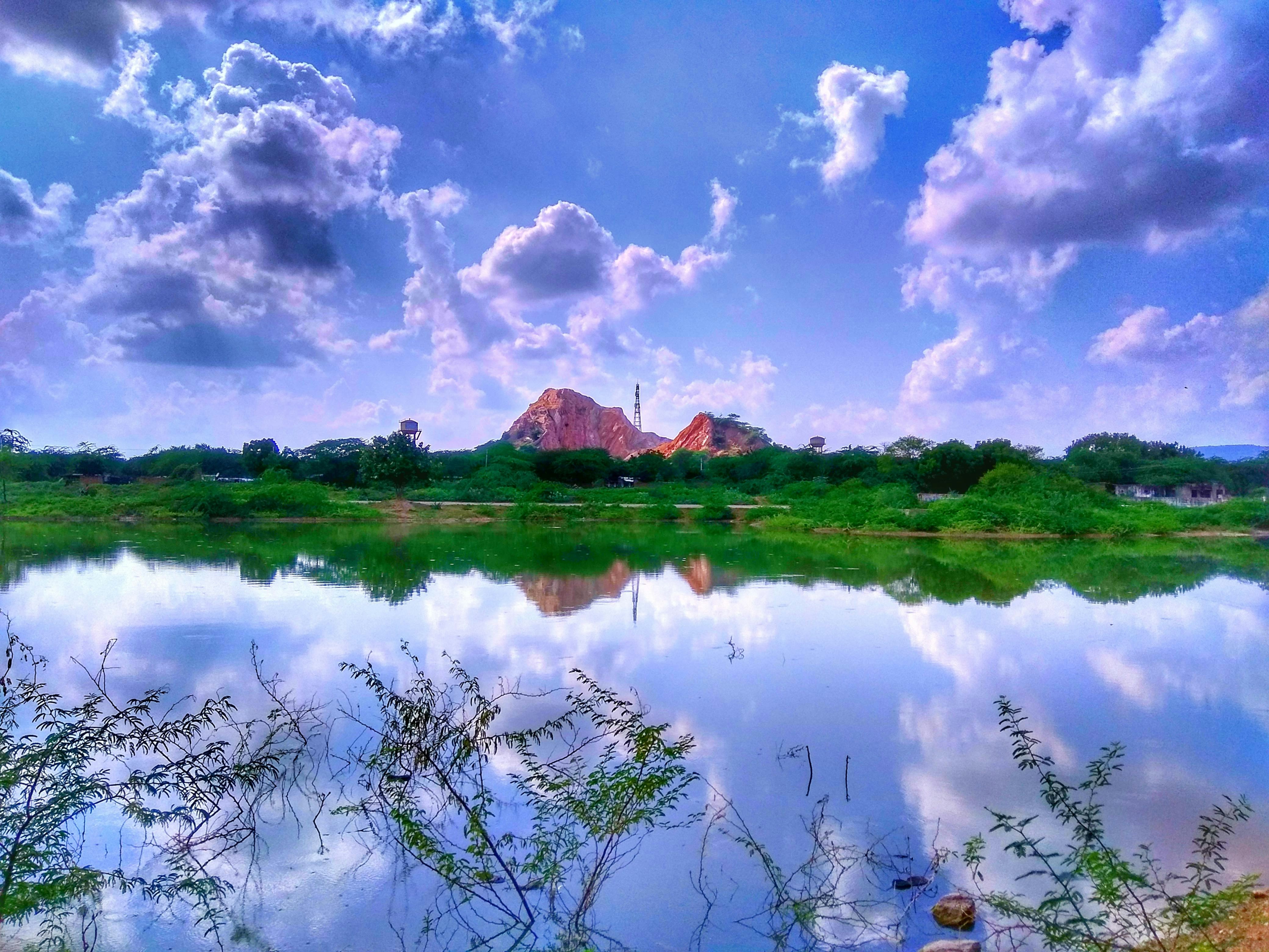 Verdant landscape with distant mountains reflected in a tranquil lake under a vivid blue sky.