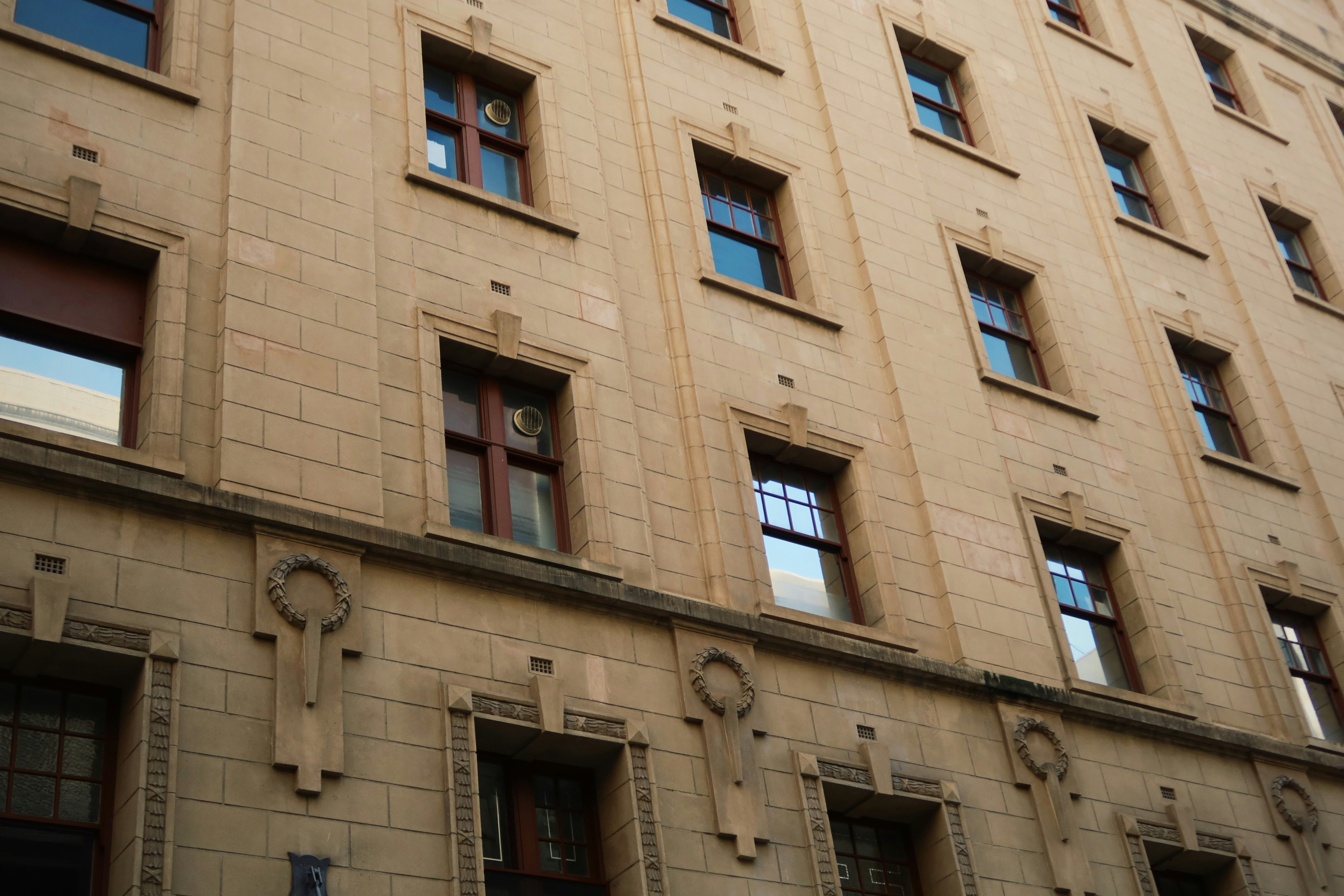 Tall sandstone facade with orderly rows of rectangular windows and subtle circular embellishments, captured in soft daylight.