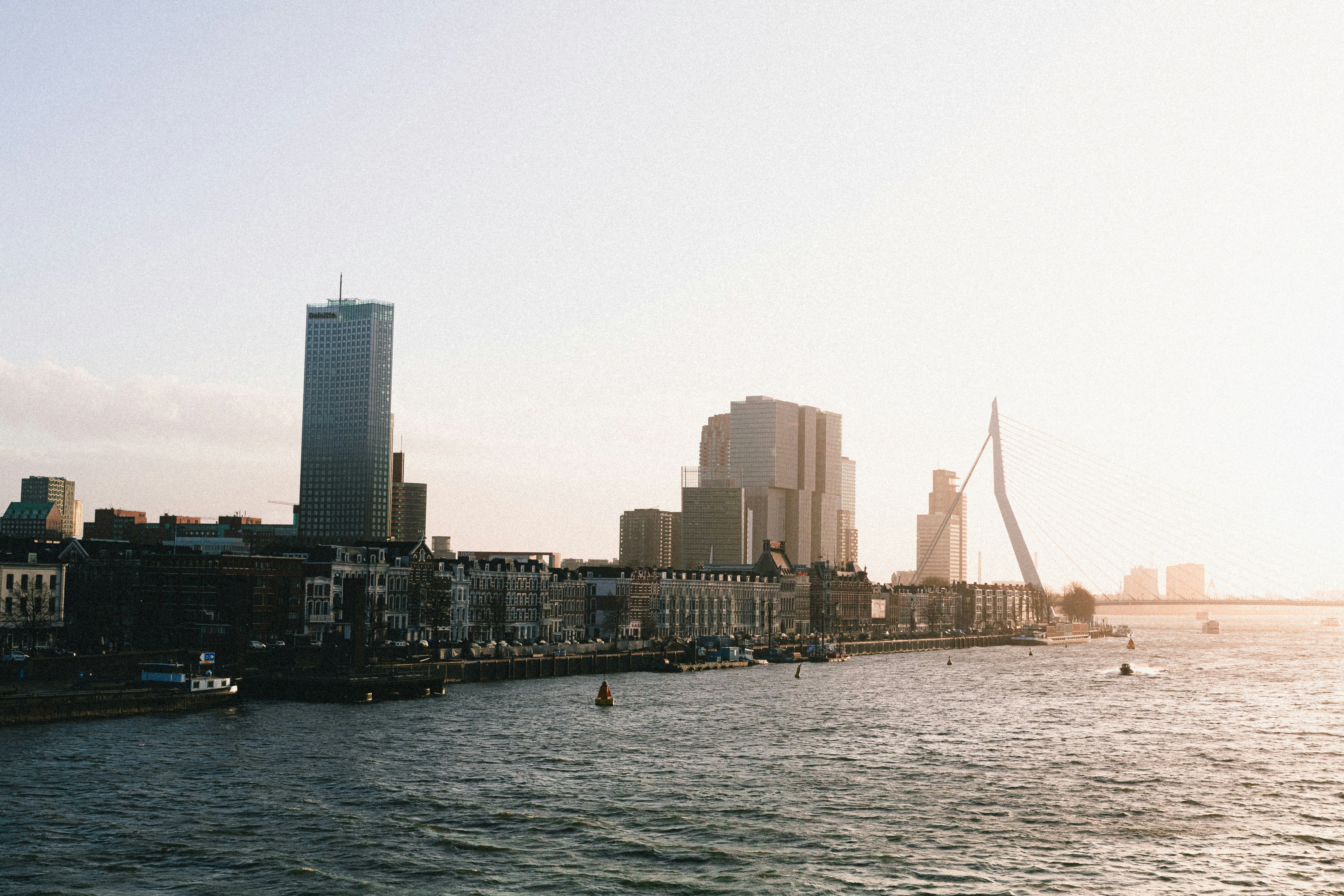 White boat gliding on water near modern city skyline at sunset.