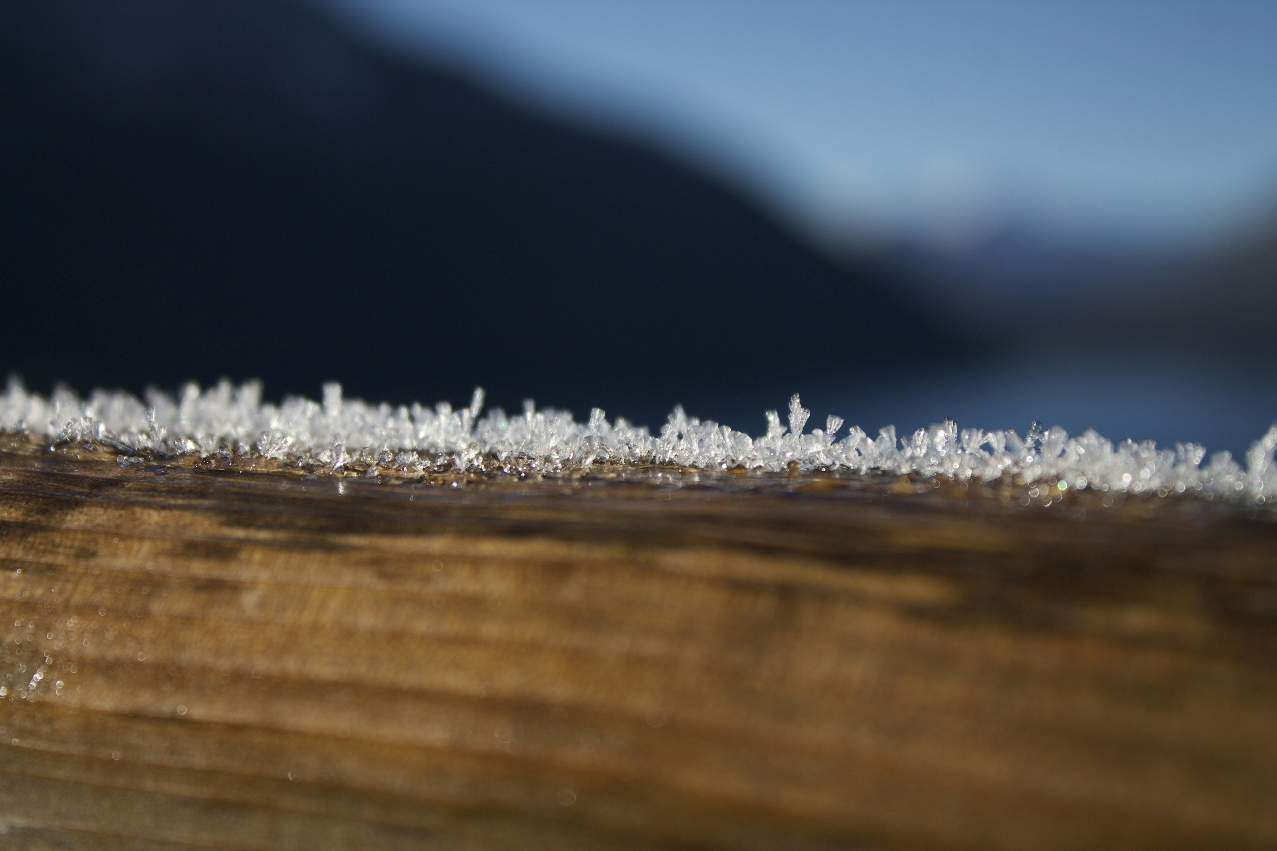 Crystals of frost lining a wooden surface against a blurred mountain backdrop.