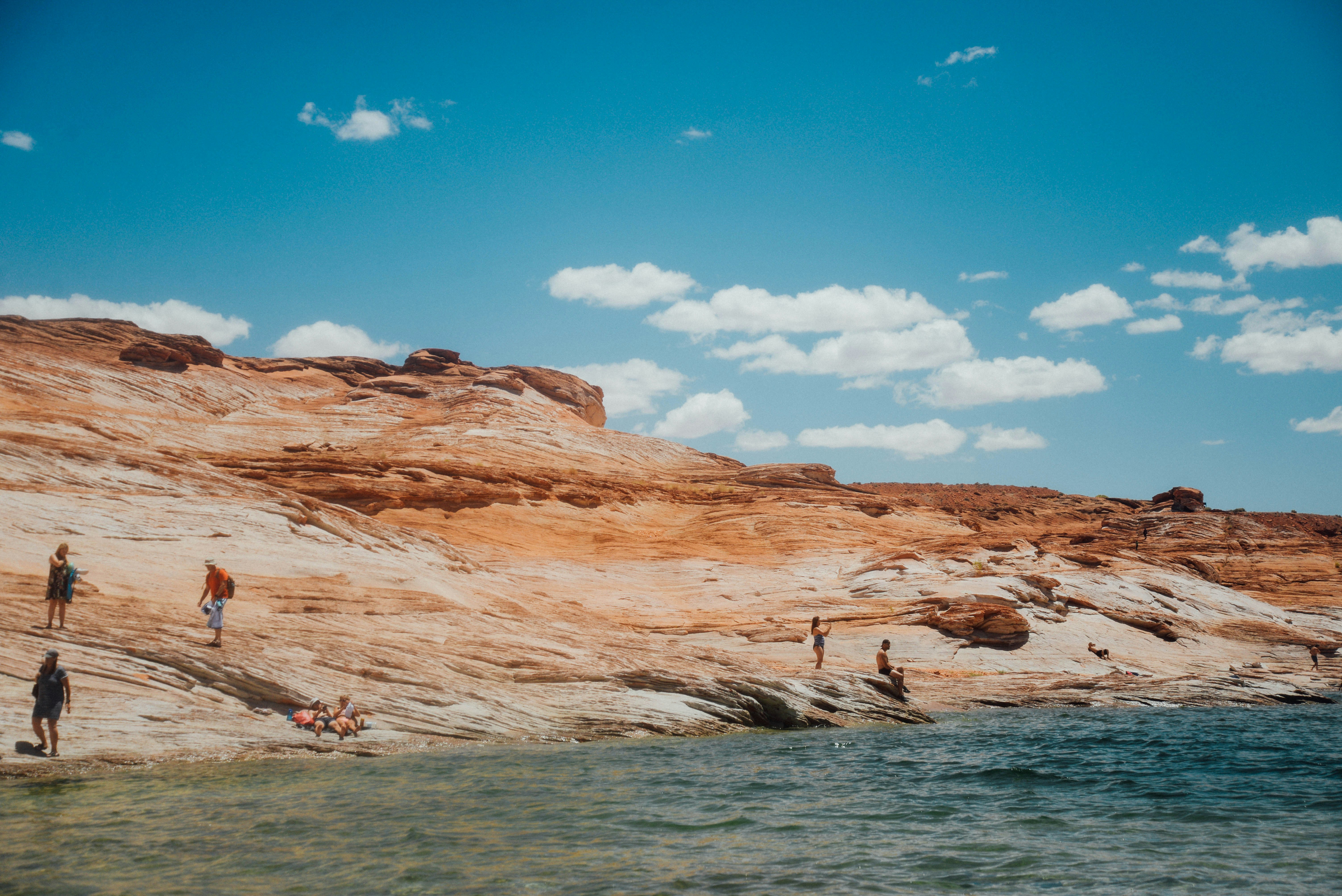 People explore a rocky shoreline under a clear blue sky with scattered clouds.