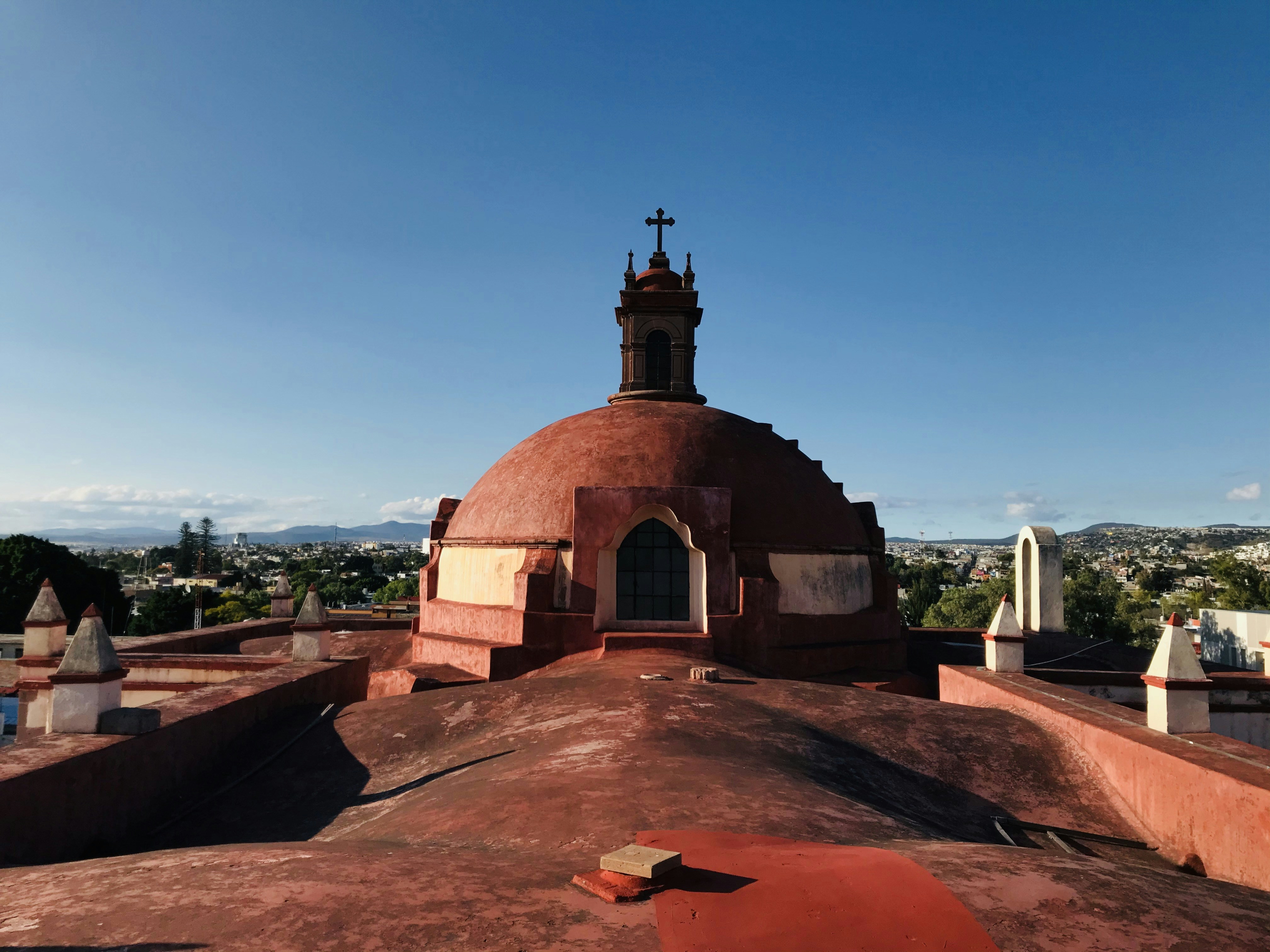 Red dome of a historic building under a clear blue sky, showcasing architectural details and surrounding landscape.