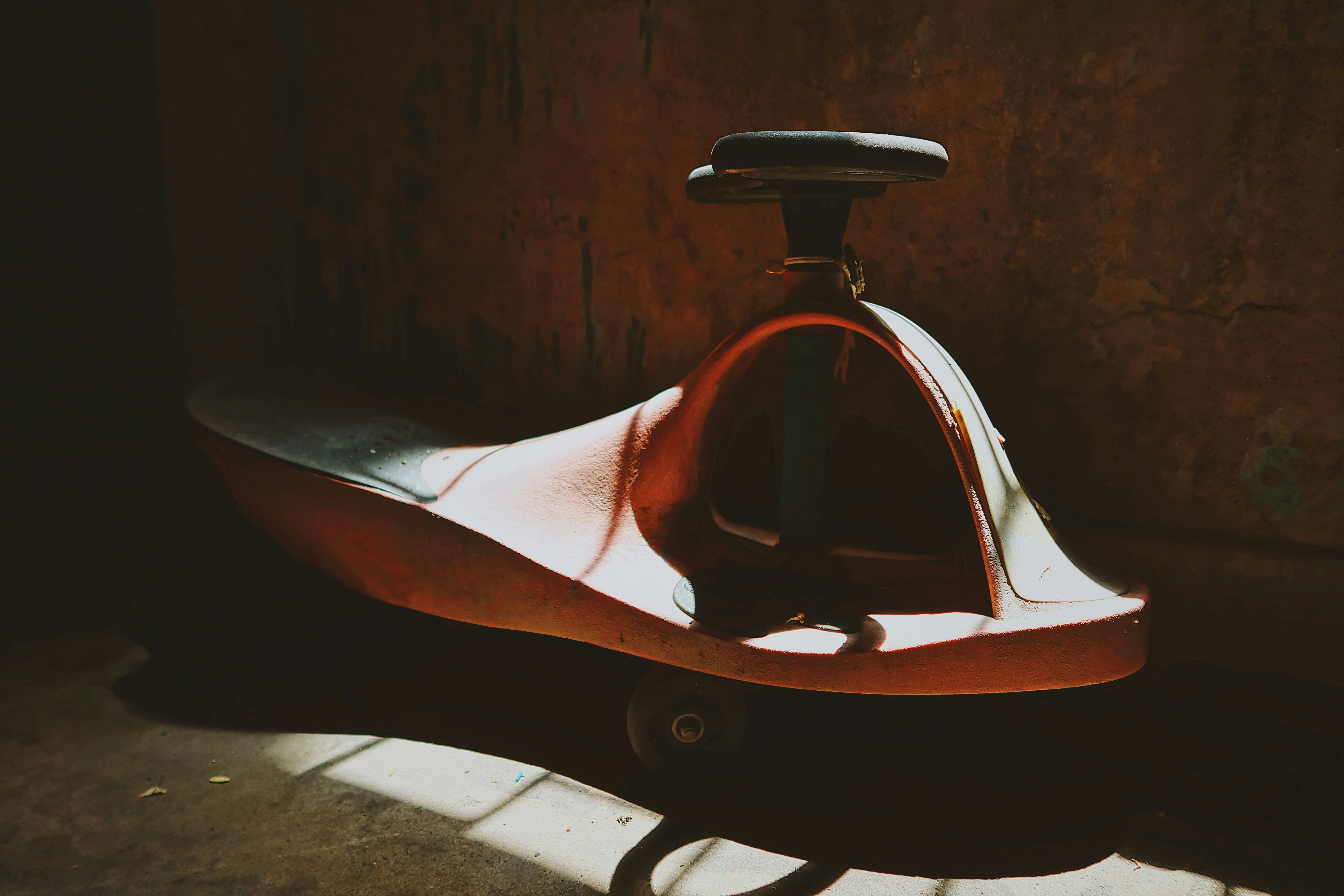 A photograph of a vintage red scooter illuminated by a single beam of light in a dark space.