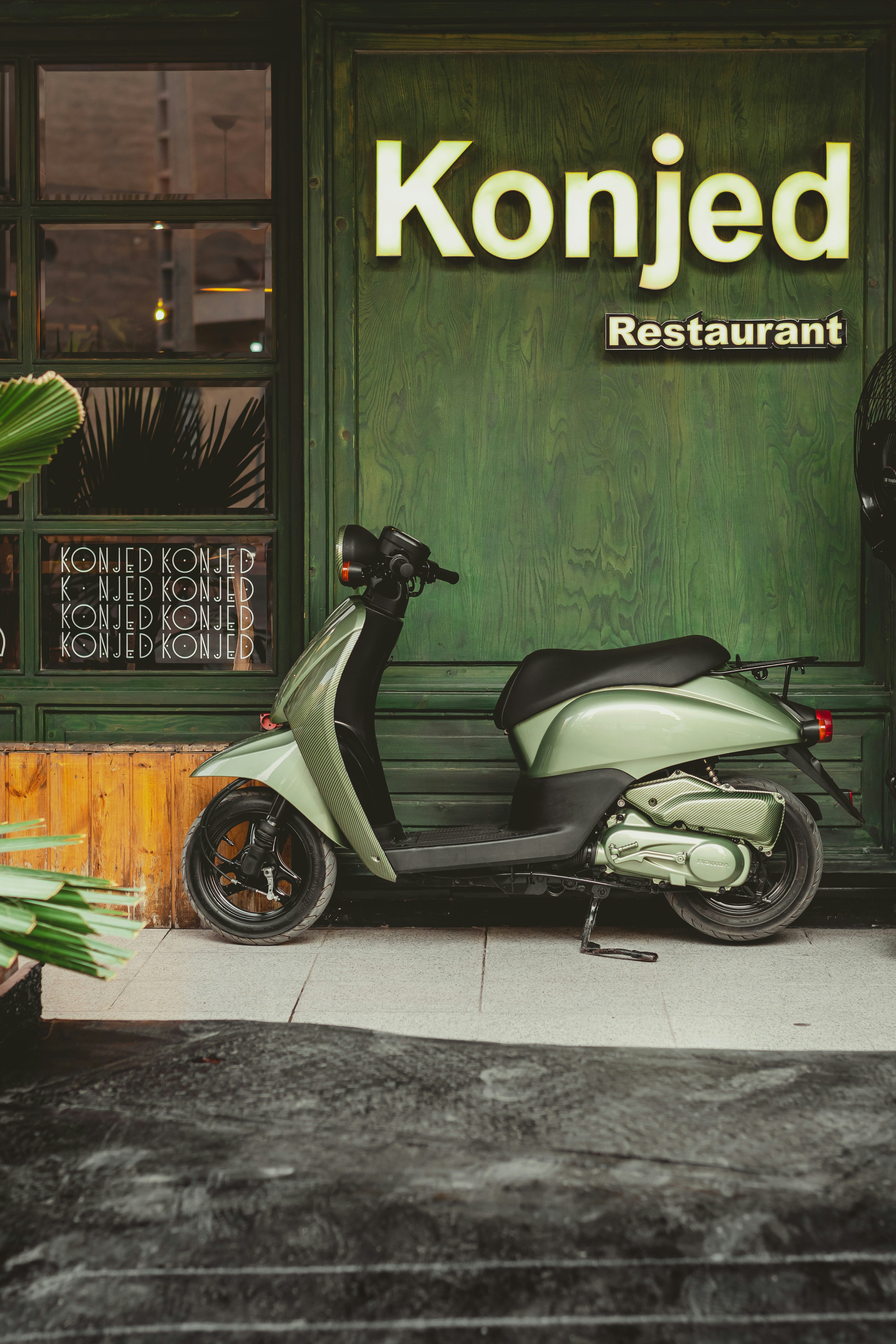 A green motorcycle in front of Konjed restaurant's green wooden wall