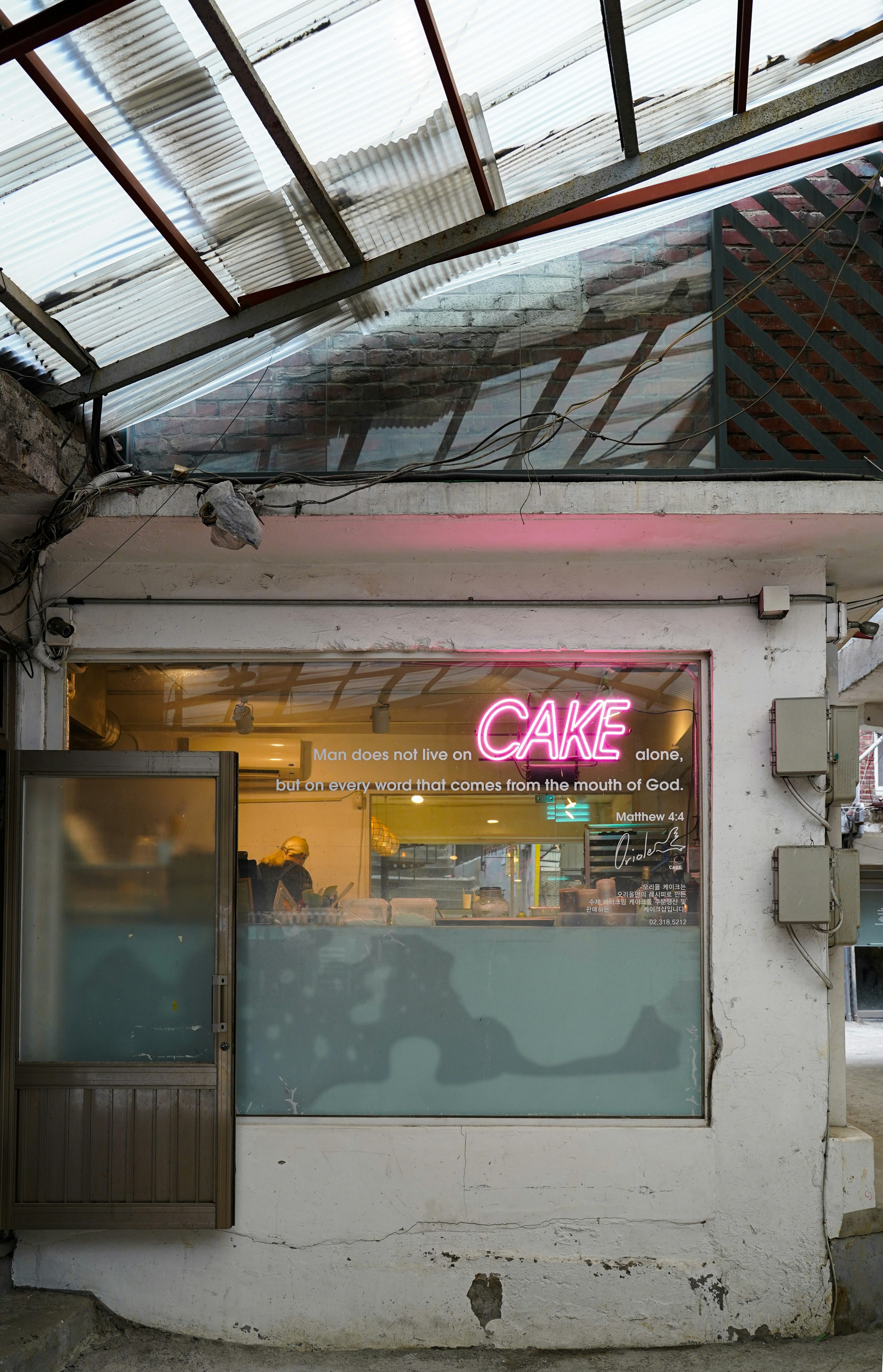 Neon CAKE Sign Illuminates a Quiet Bakery Window Under a Glass Canopy